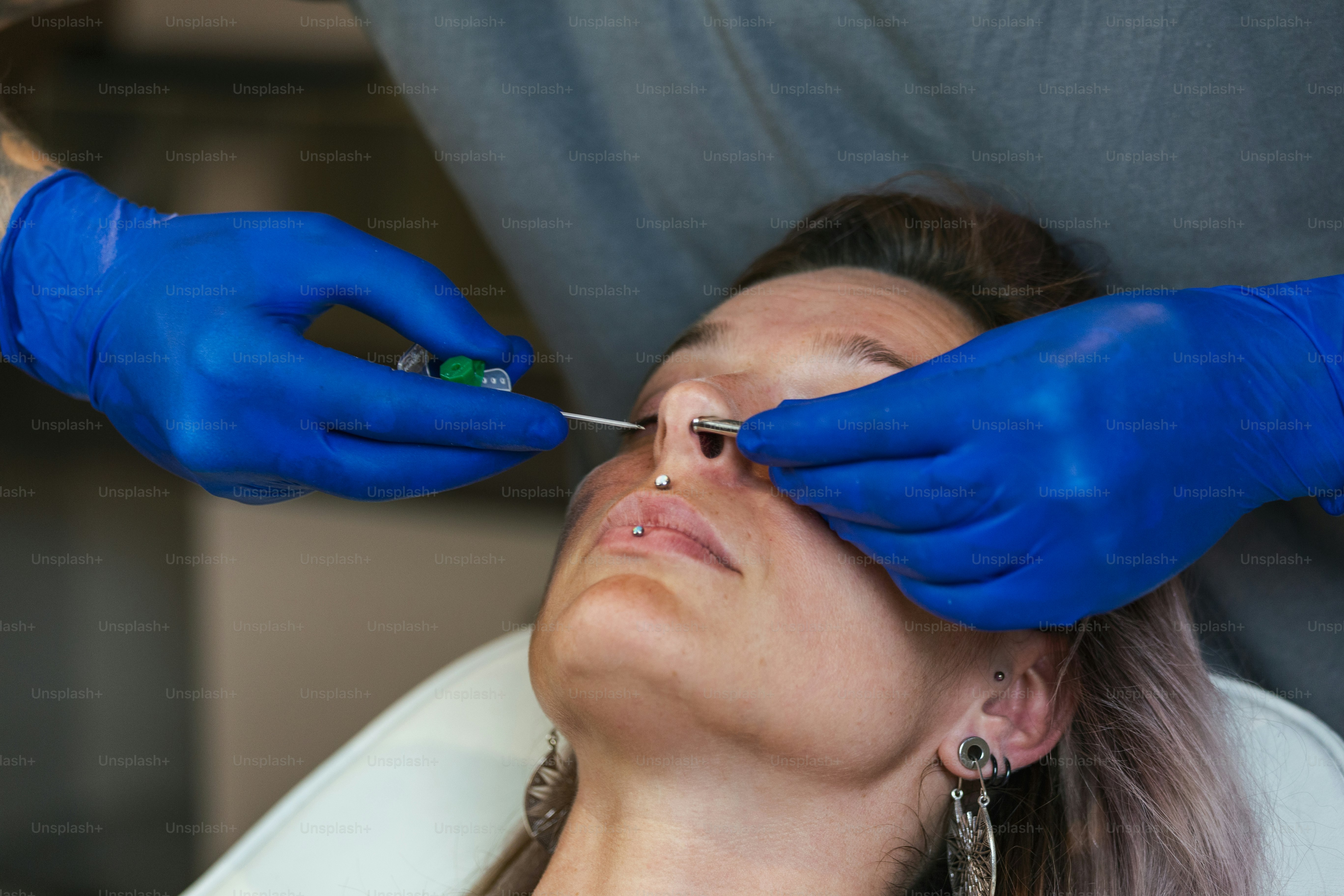 Portrait of a woman getting her nose pierced. Man showing a process of ...