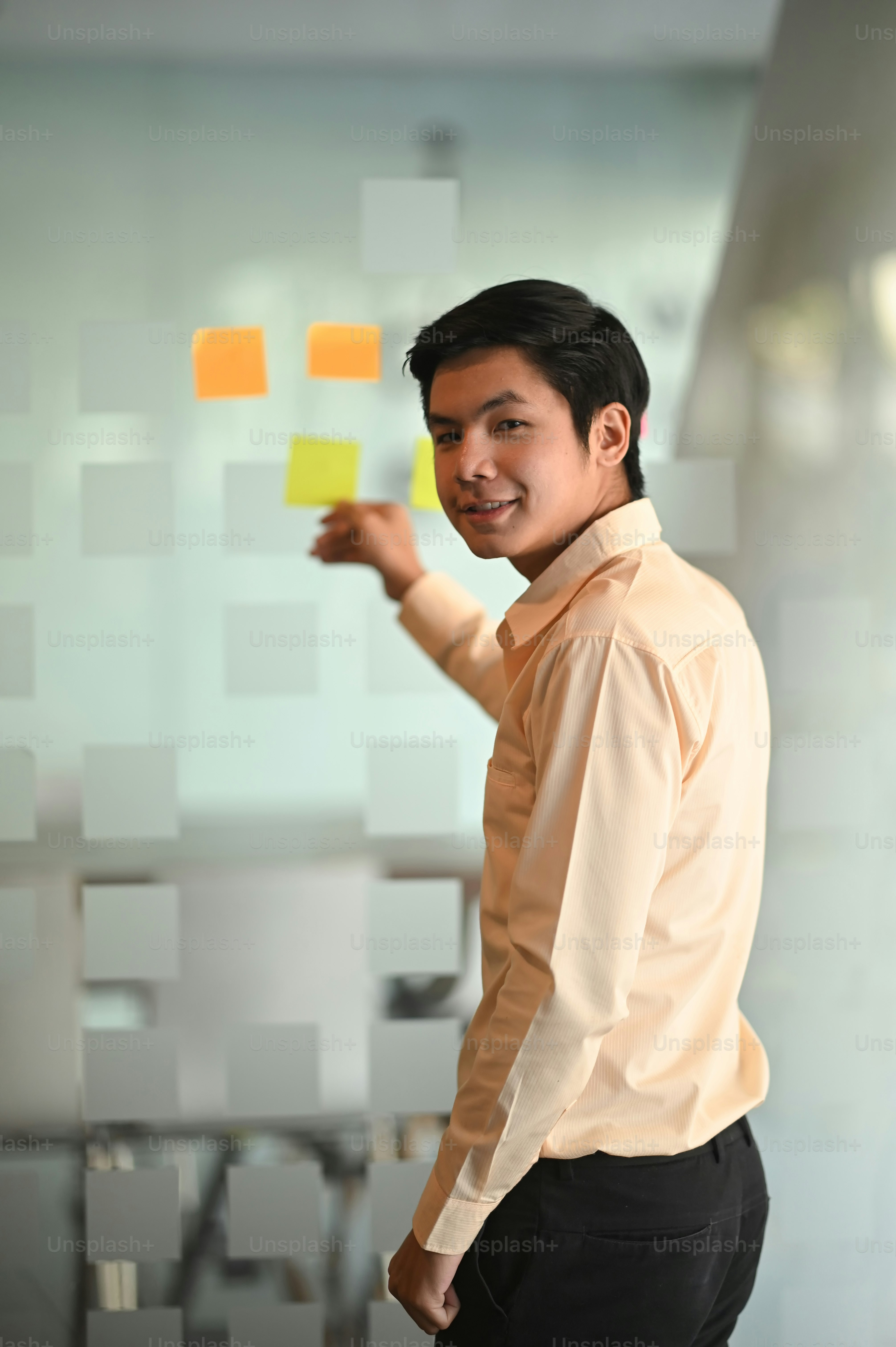 Behind shot of young creative man sticky notes at the glass wall and ...