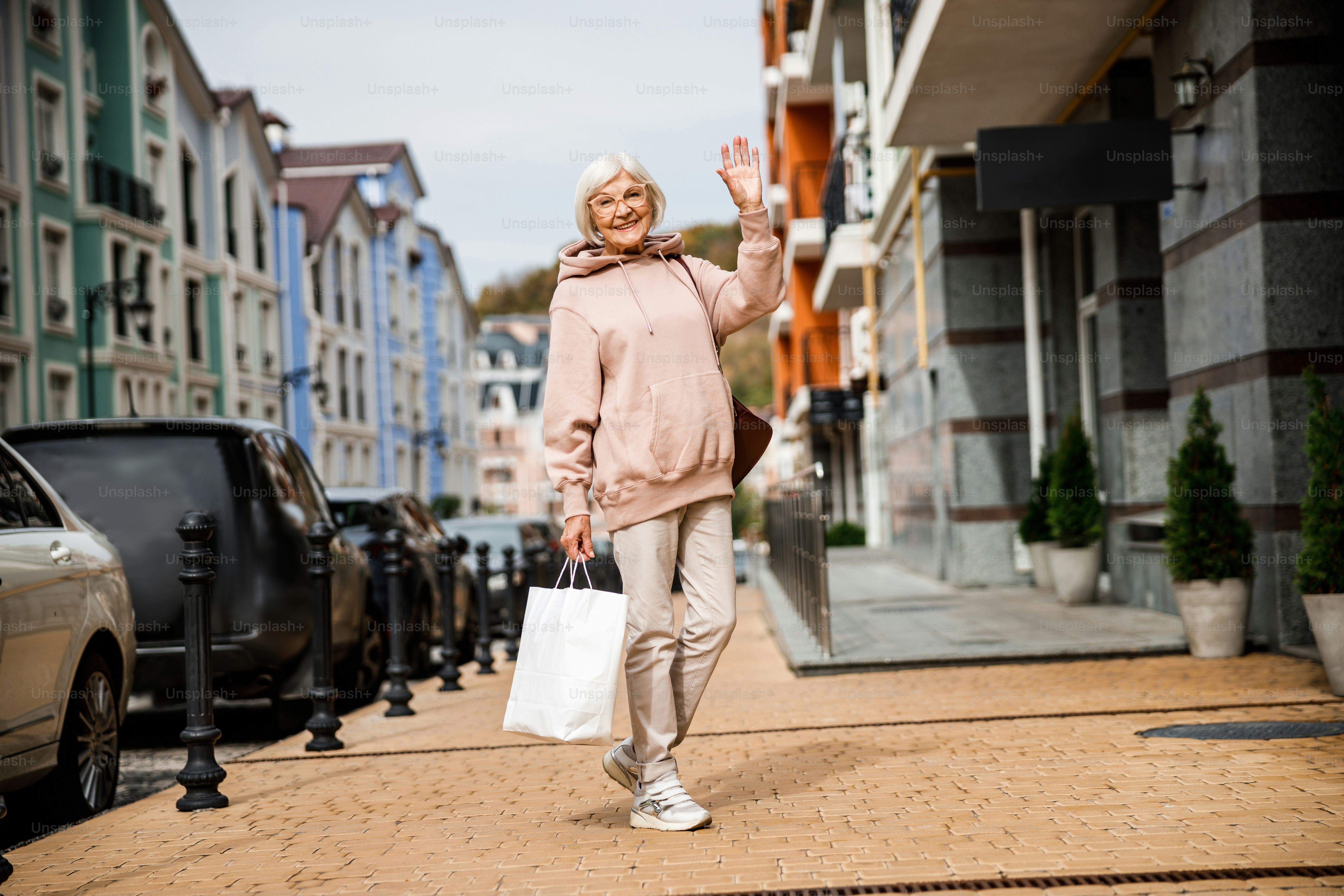 Cheerful aged lady in sporty clothes is waving hello during walk in ...
