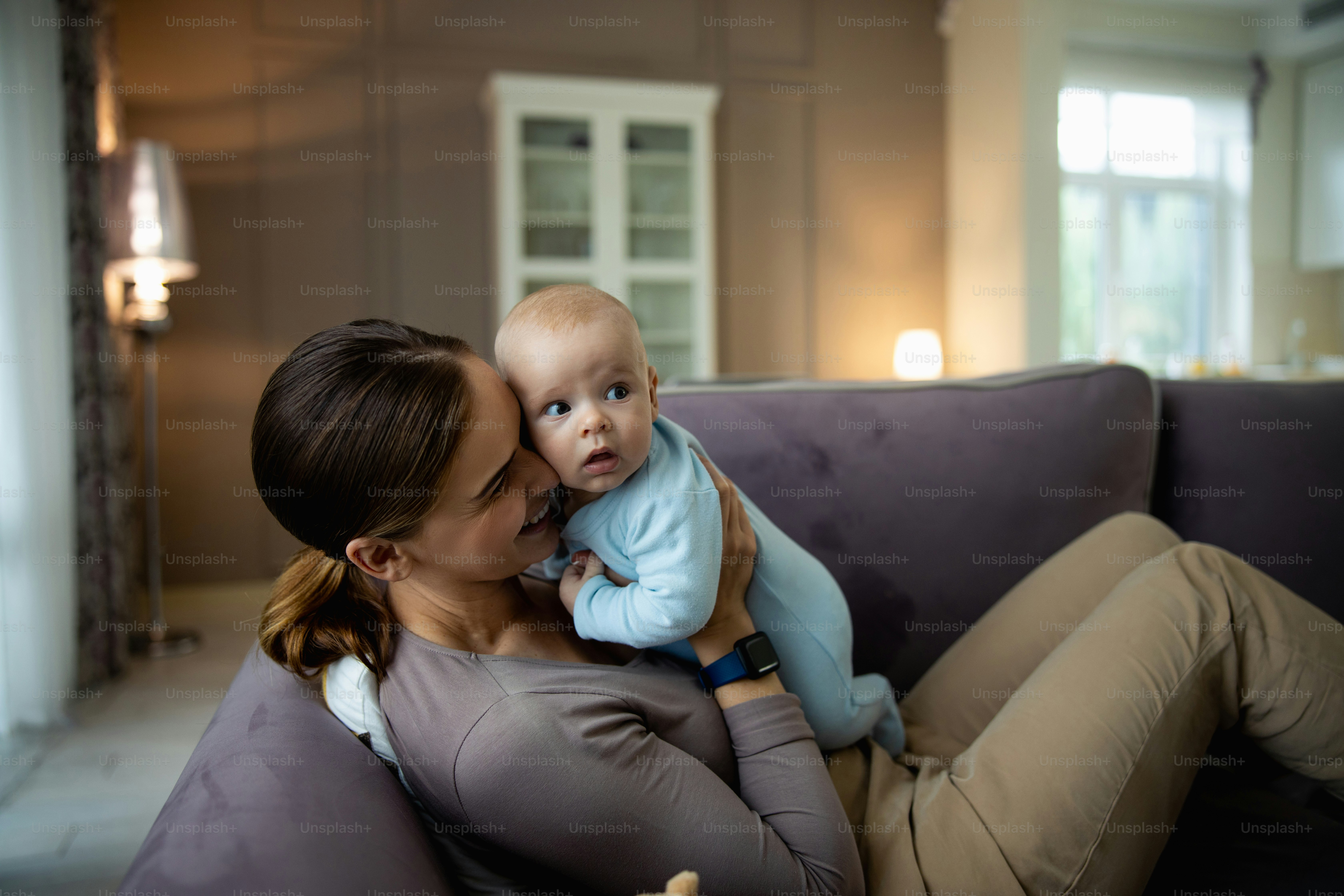 Happy beautiful woman hugging her child while resting on sofa stock ...