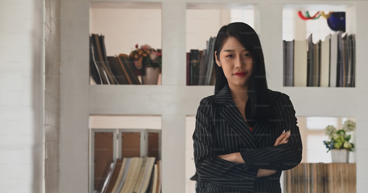 검은 줄무늬 정장을 입은 멋진 사업가가 현대적인 책장을 배경으로 팔짱을 끼고 서 있다 임원 여성 Ceo 비즈니스 보드 개념
