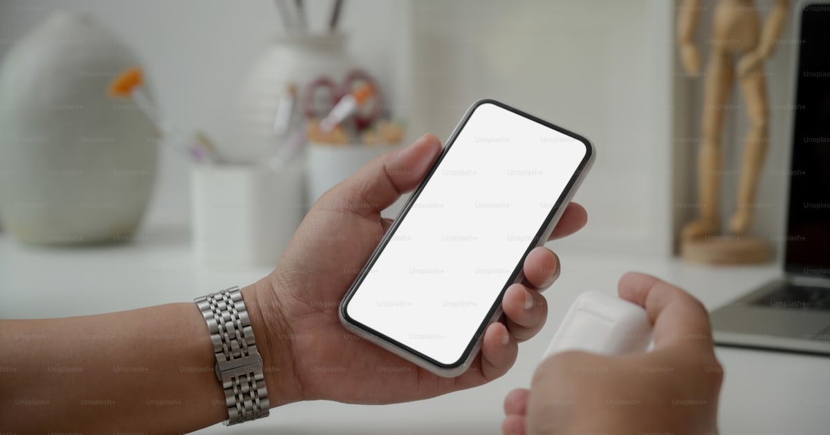 最小限の職場に座ってワイヤレス ヘッドフォンと空白の画面のスマート フォンを保持している男性アーティストのショットをトリミングの写真 タイ