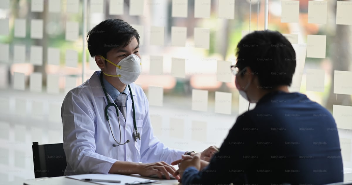 검사실을 배경으로 의사 작업 책상에 함께 앉아 있는 동안 젊은 환자 남자와 이야기토론하는 의사의 잘린 이미지 사진