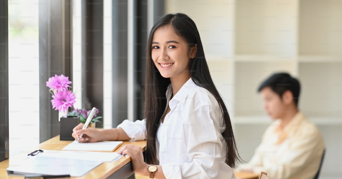 사무실에서 동료와 함께 나무 카운터 바에 앉아 문서 파일에 글을 쓰는 회계사로 일하는 젊은 아름다운 여성의 사진 사진