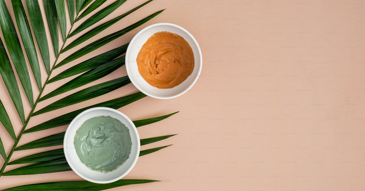 Skincare 순수한 점토 얼굴 마스크는 복숭아 배경에 열대 야자 잎 천연 유기농 스파 화장품 얼굴 피부 치료 개념 플랫