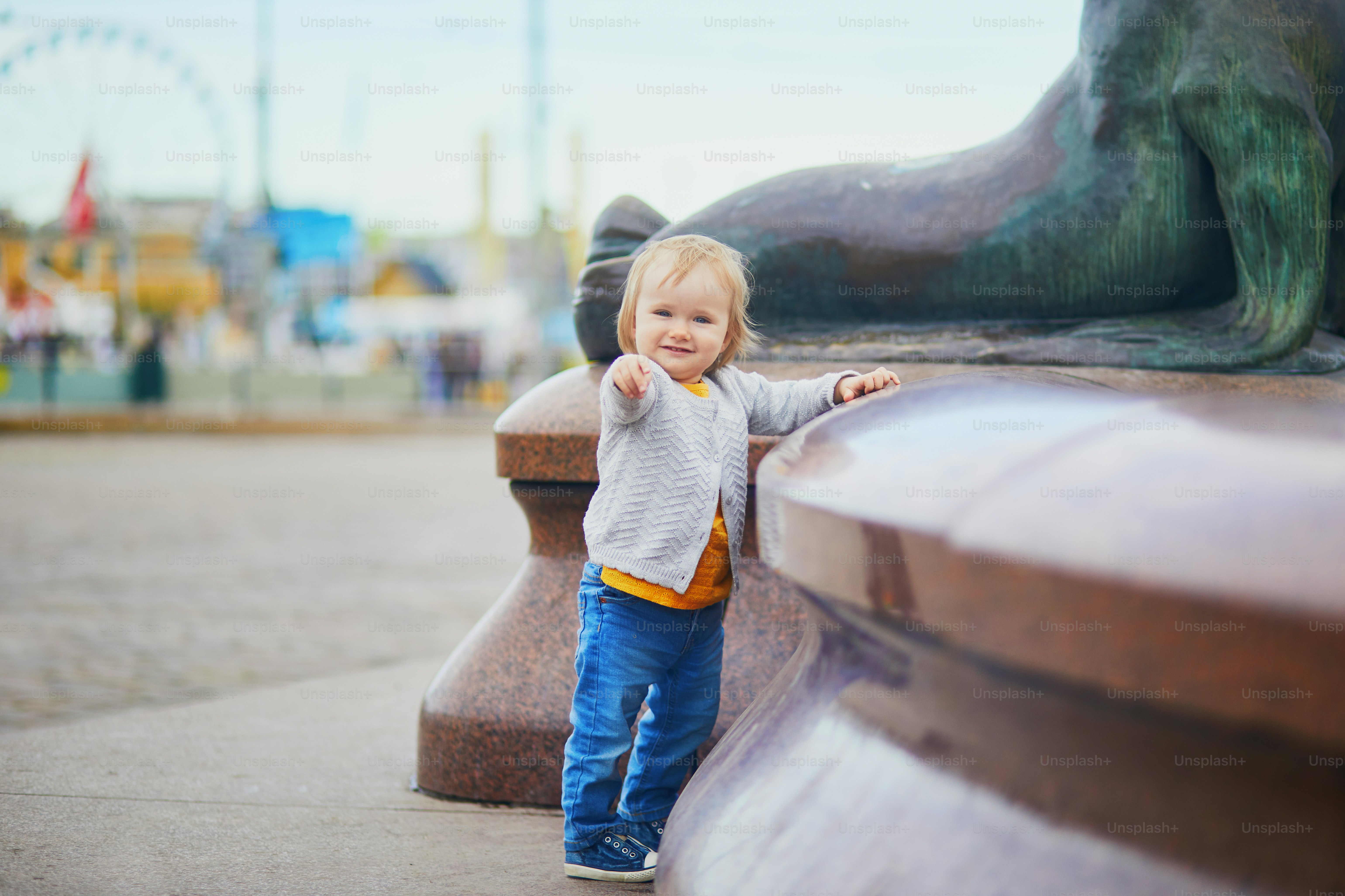 Little baby girl standing close to city fountain on a street. Toddler ...