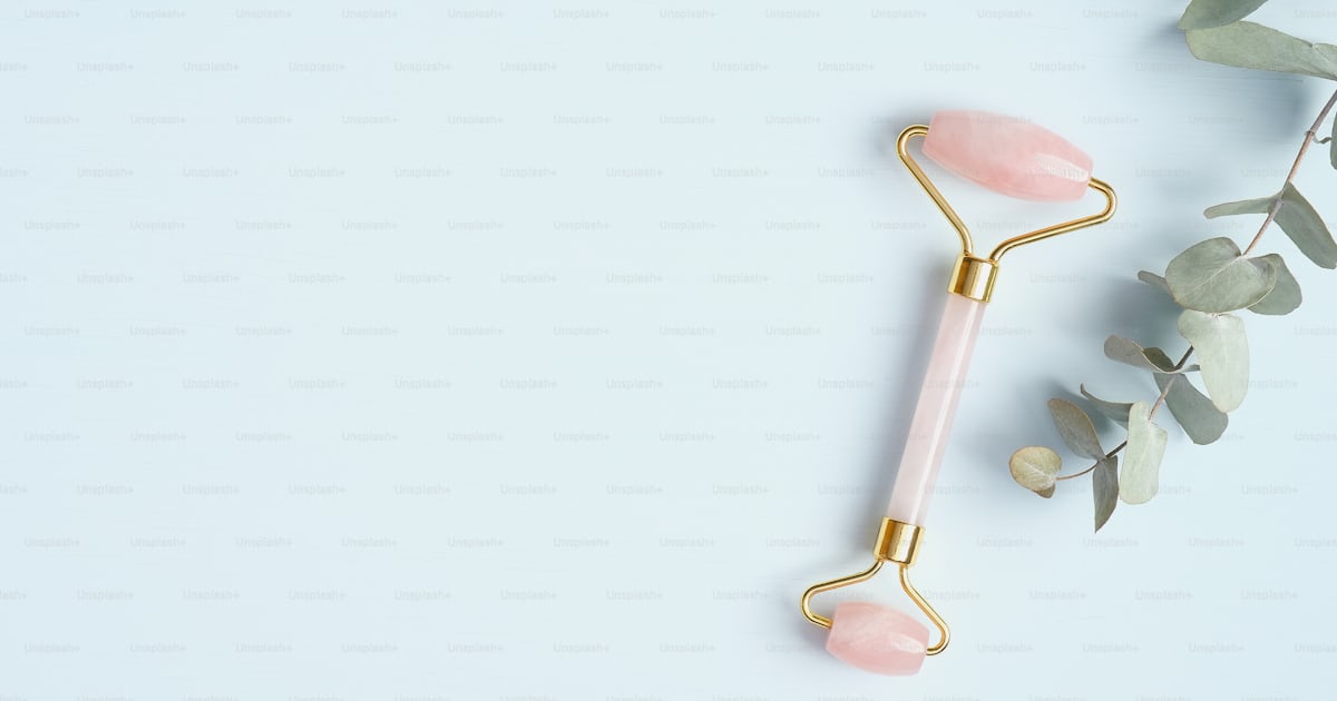 파란색 배경에 유칼립투스 잎이 있는 로즈 쿼츠 페이셜 롤러 옥 얼굴 마사지 노화 방지 주름 방지 미용 스킨 케어 도구 사진