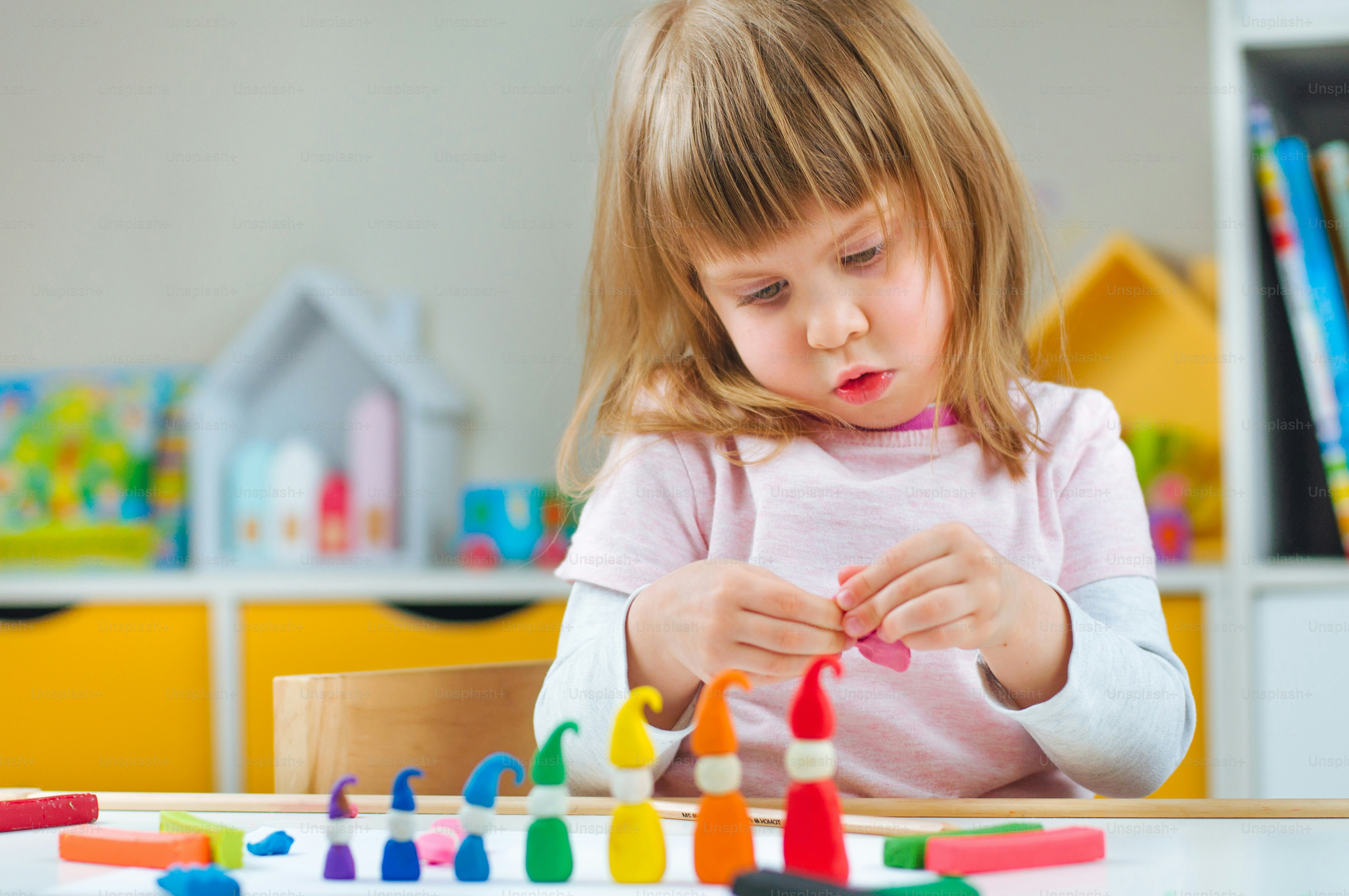 Little girl molding colorful gnomes from child's play clay on the table ...