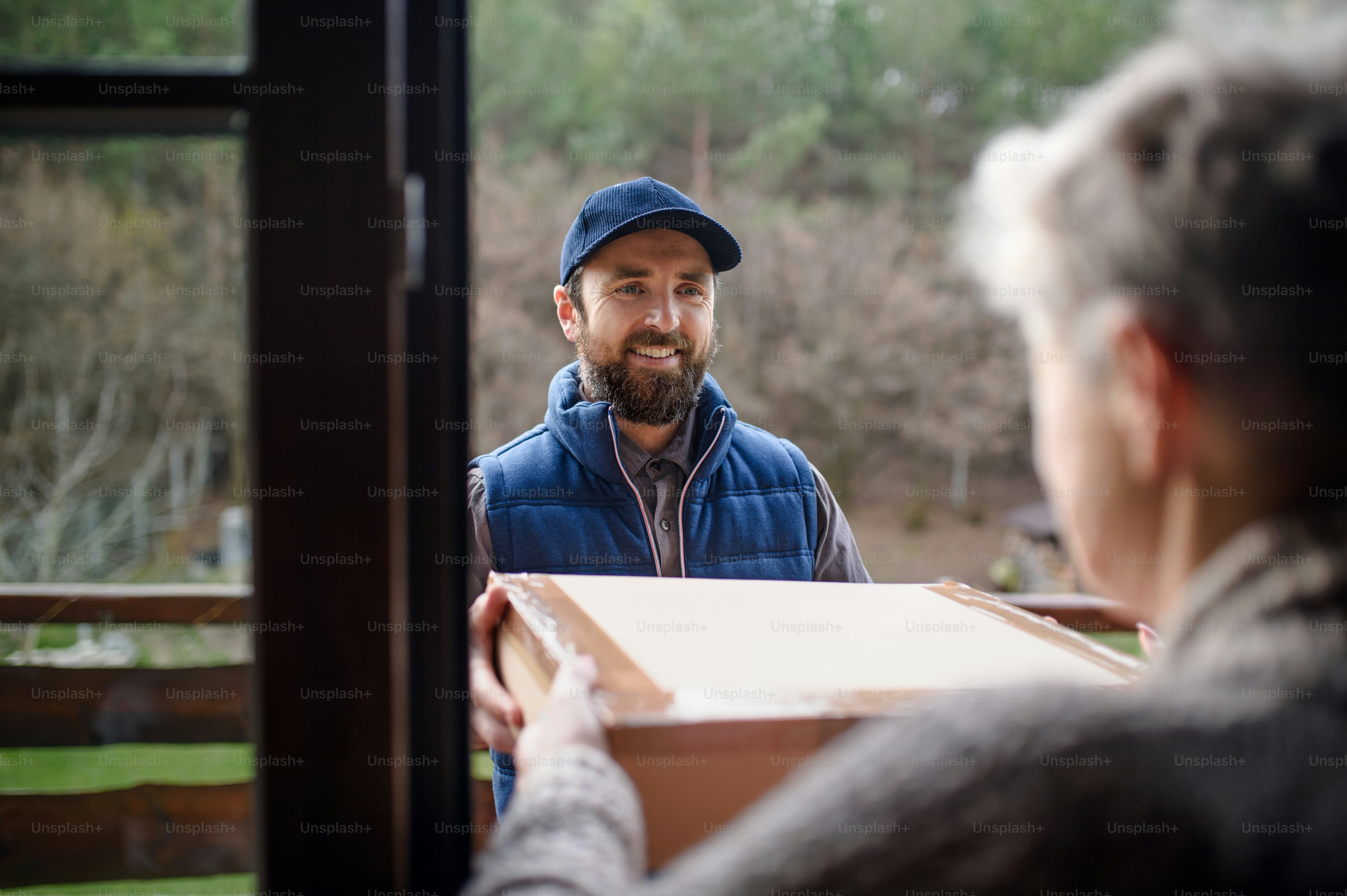 Man courier delivering parcel box to senior woman, standing by doorstep ...