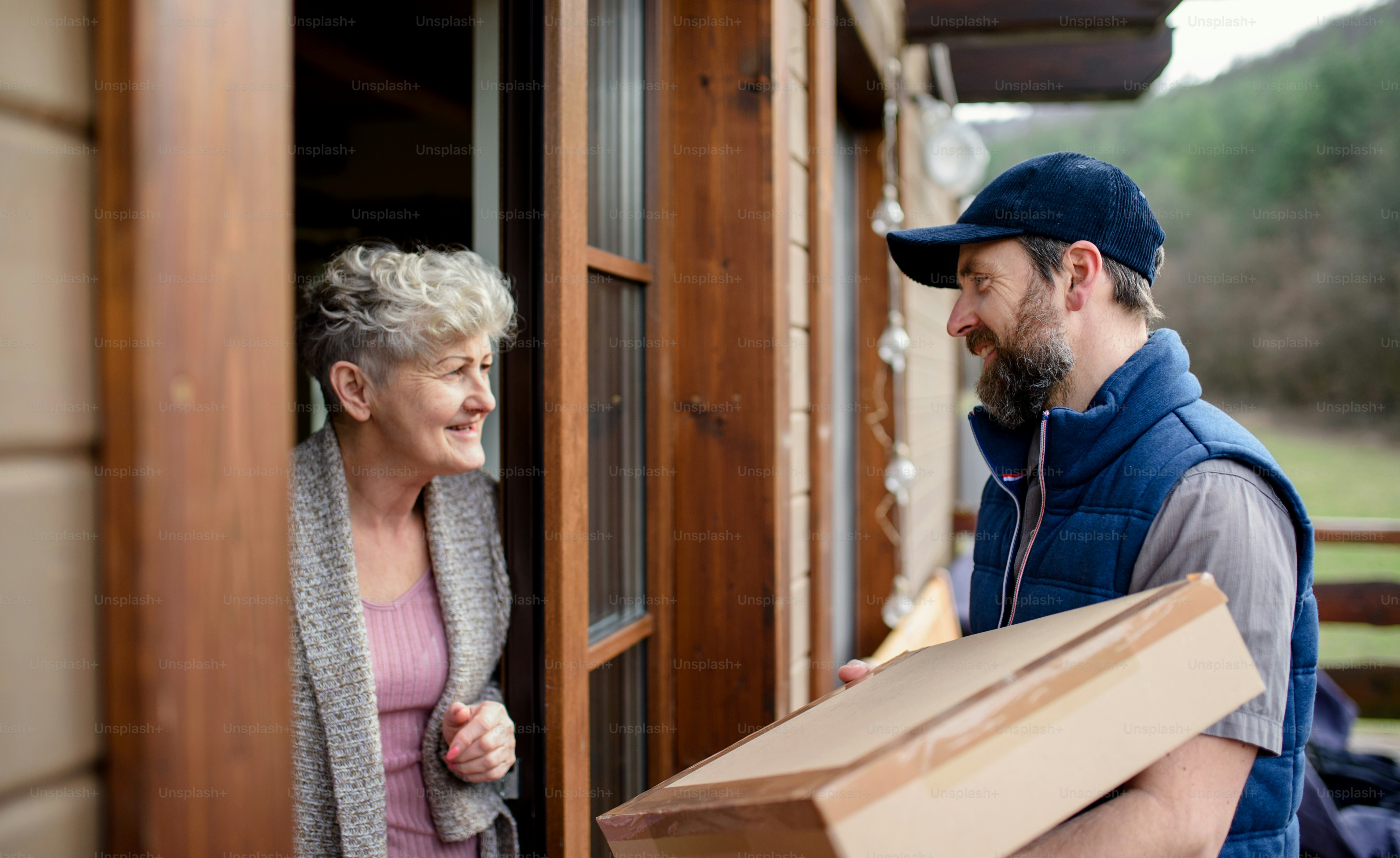 Man courier delivering parcel box to senior woman, standing by doorstep ...