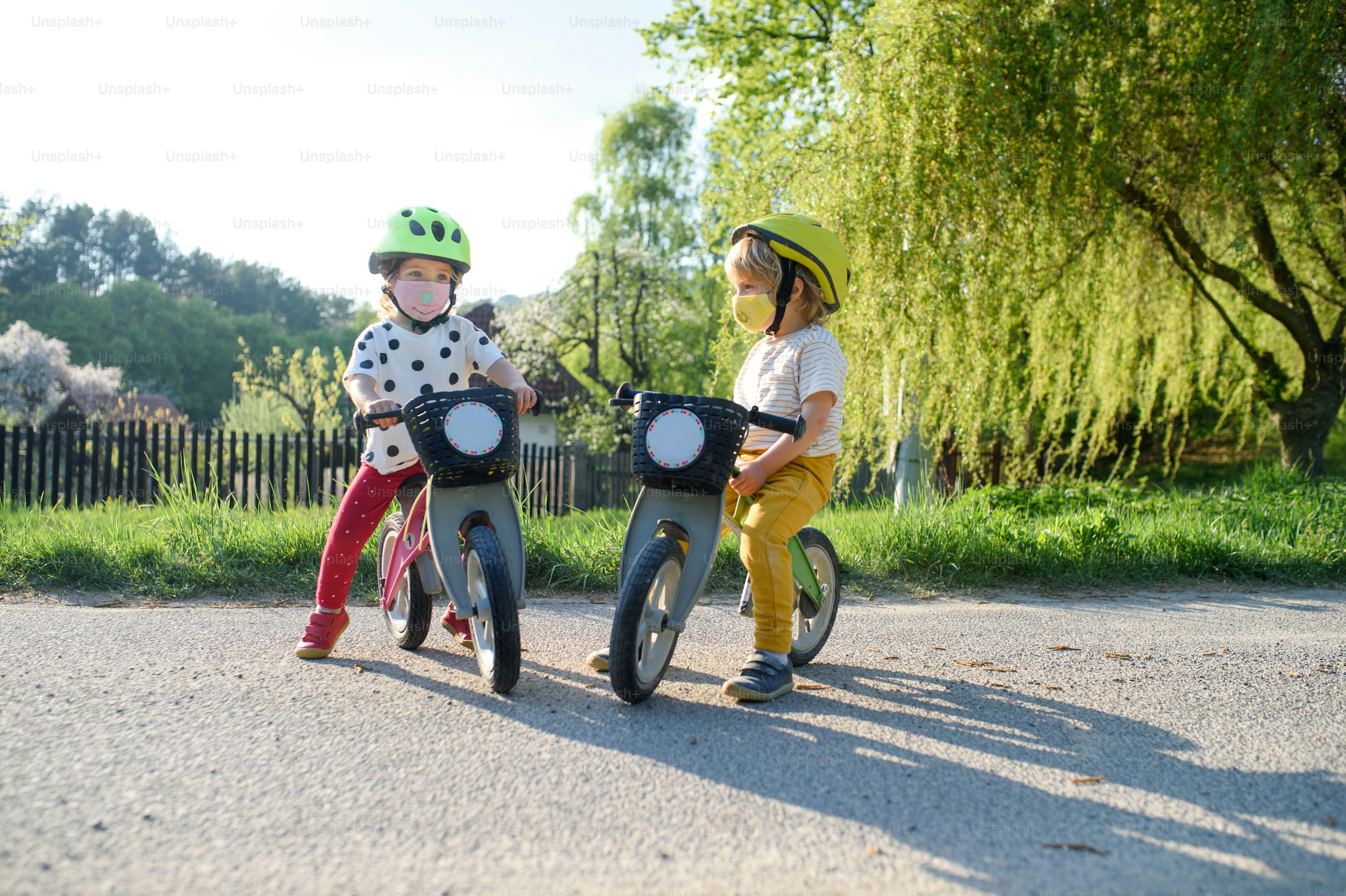 Small children boy and girl with face masks playing outdoors with bike ...