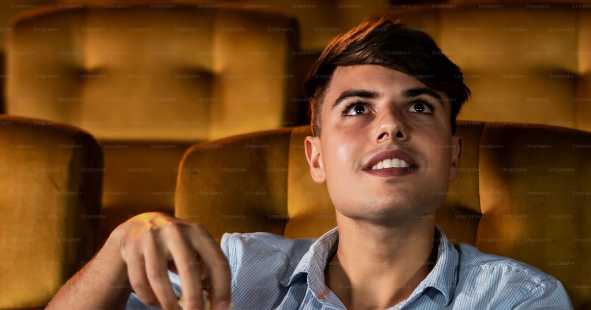 A Young Man Smiling Enjoying With His Popcorn While Watching A Movie In