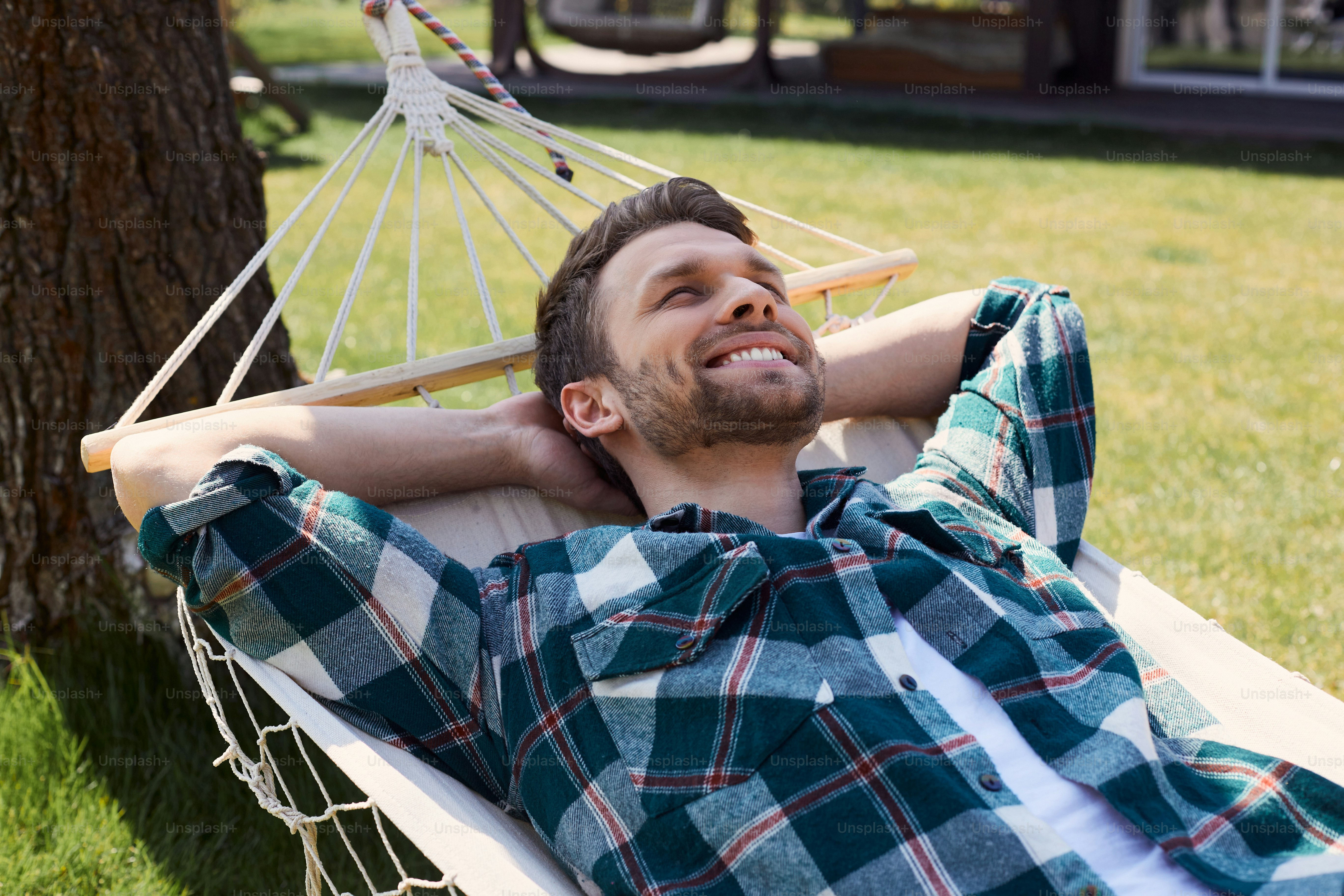 Joyful bearded male looking upwards and keeping hands behind his head ...