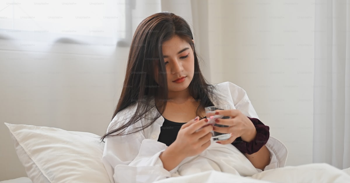아픈 여자가 침대에서 알약을 먹은 후 물 한 잔을 들고 있습니다 사진 Unsplash의 태국 이미지