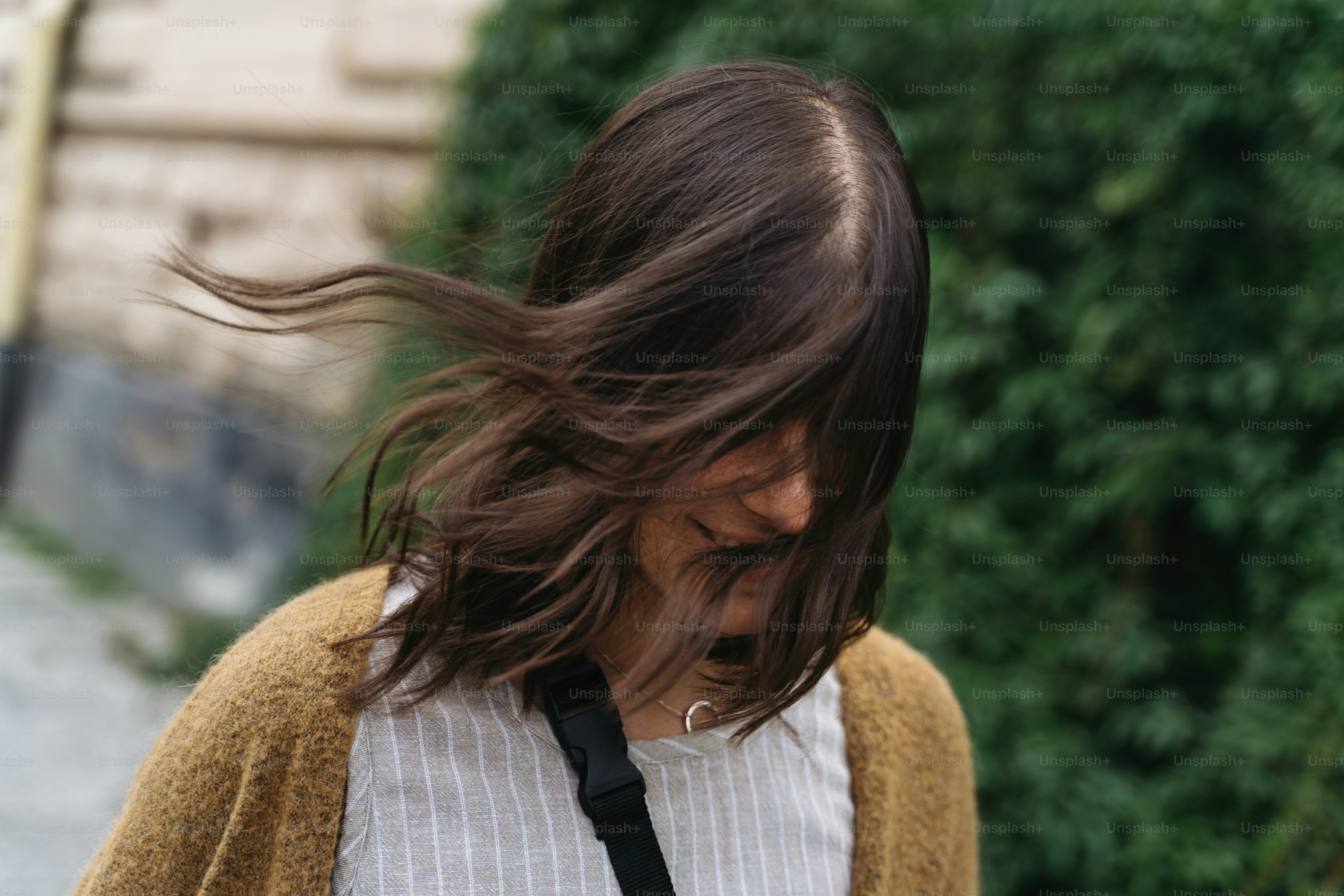 Happy stylish hipster girl walking with windy curly hair in city street ...