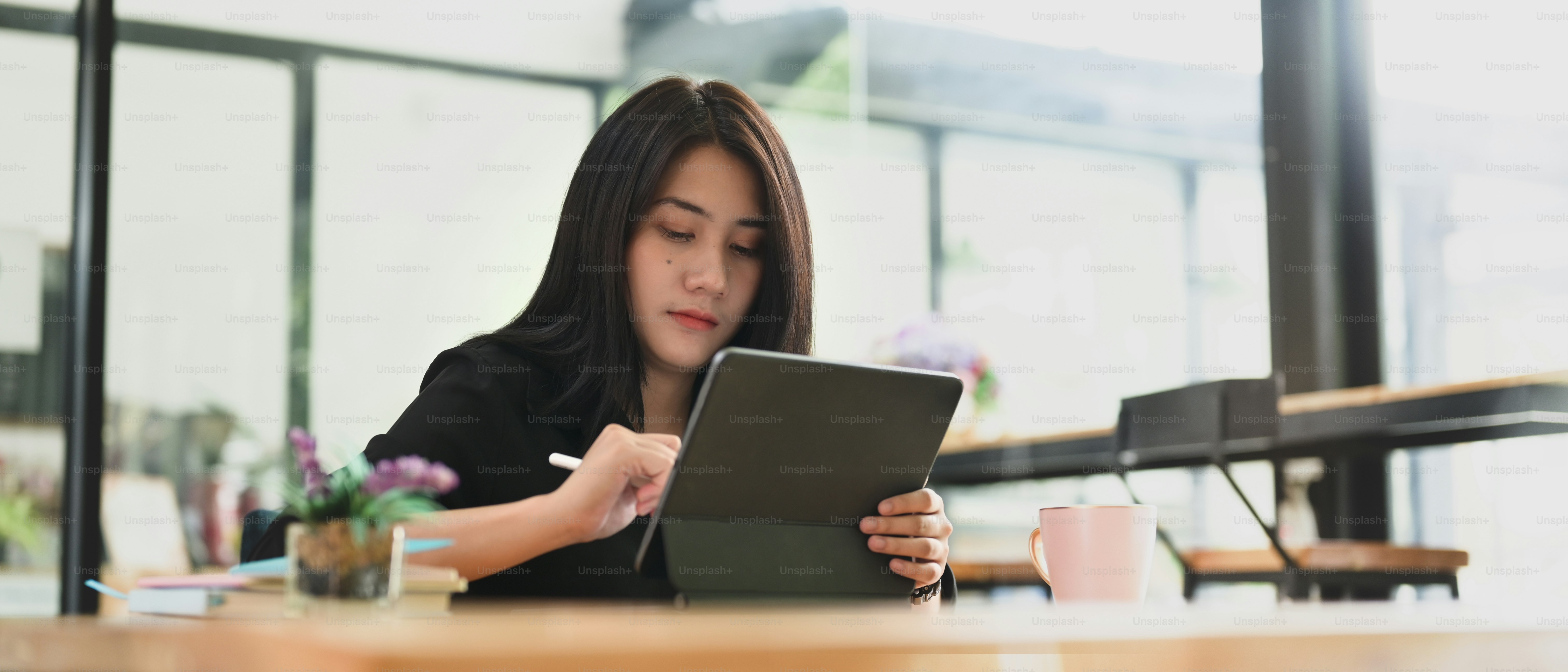 A woman is writing on a computer tablet while sitting at the wooden ...