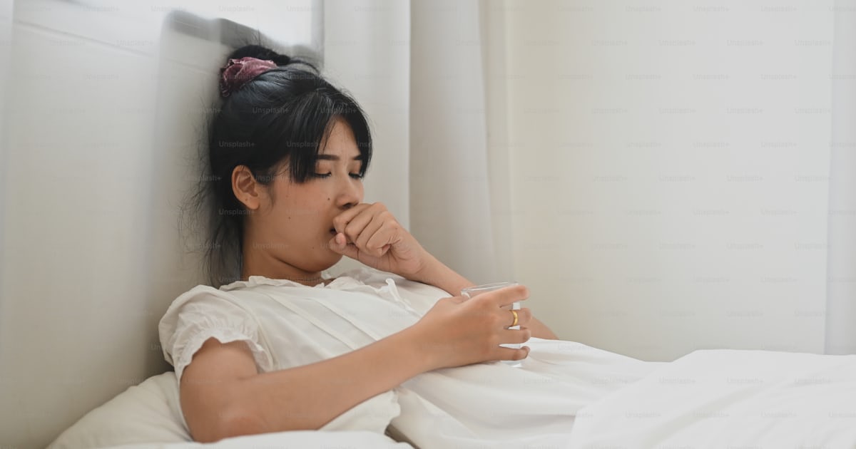 An Ill Woman Drinks Water And Consuming A Pill While Lying On The Bed