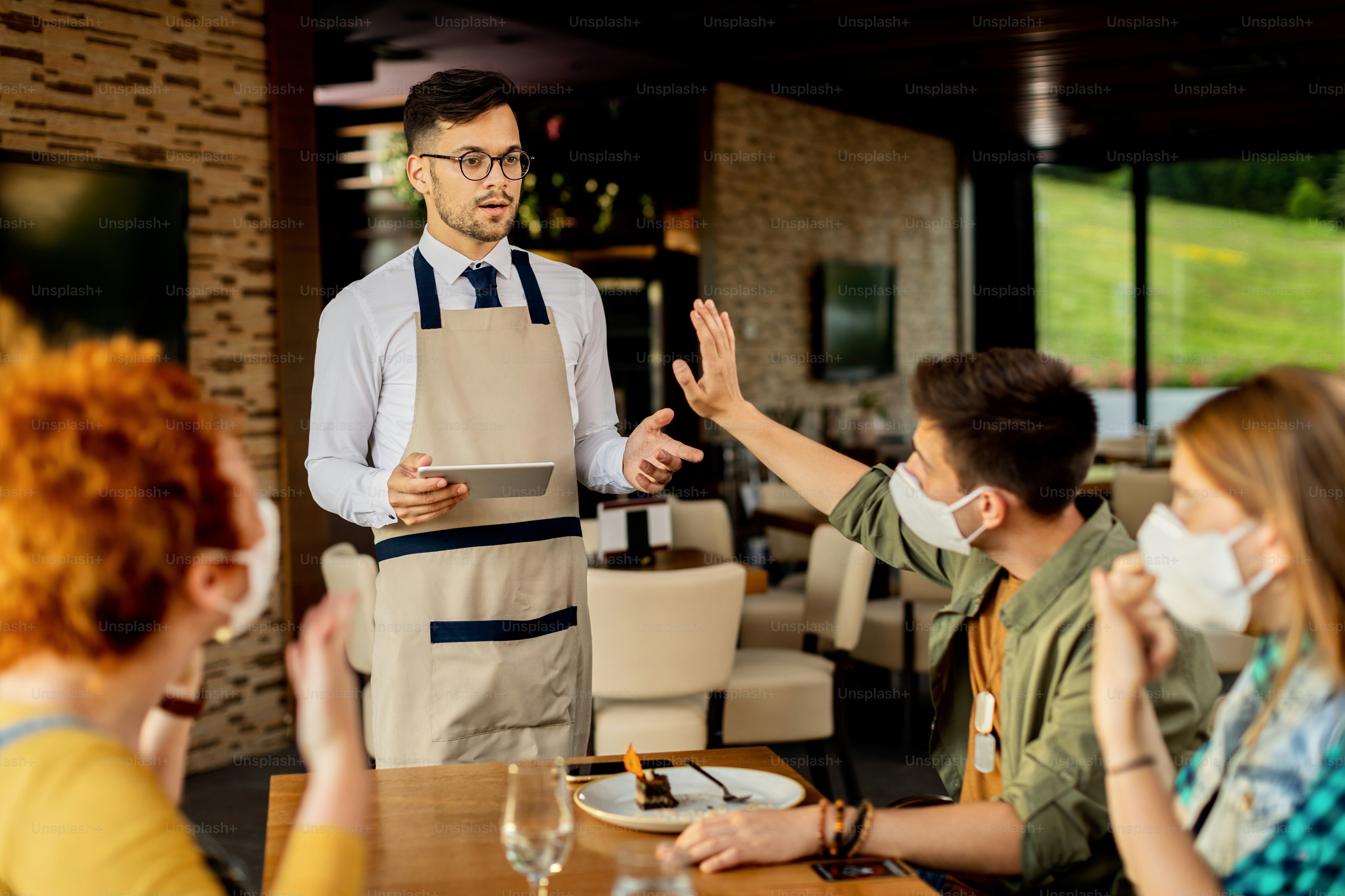 Group of customers gesturing stop sign to a waiter who is not wearing ...