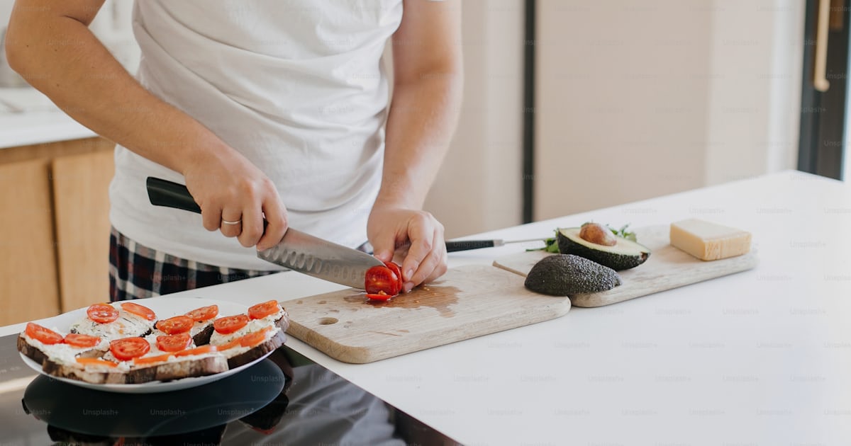 가정 요리 개념입니다 현대 흰색 부엌에서 샌드위치를 위해 토마토 슬라이스를 자르는 사람 아보카도 토마토 아루 굴라 치즈