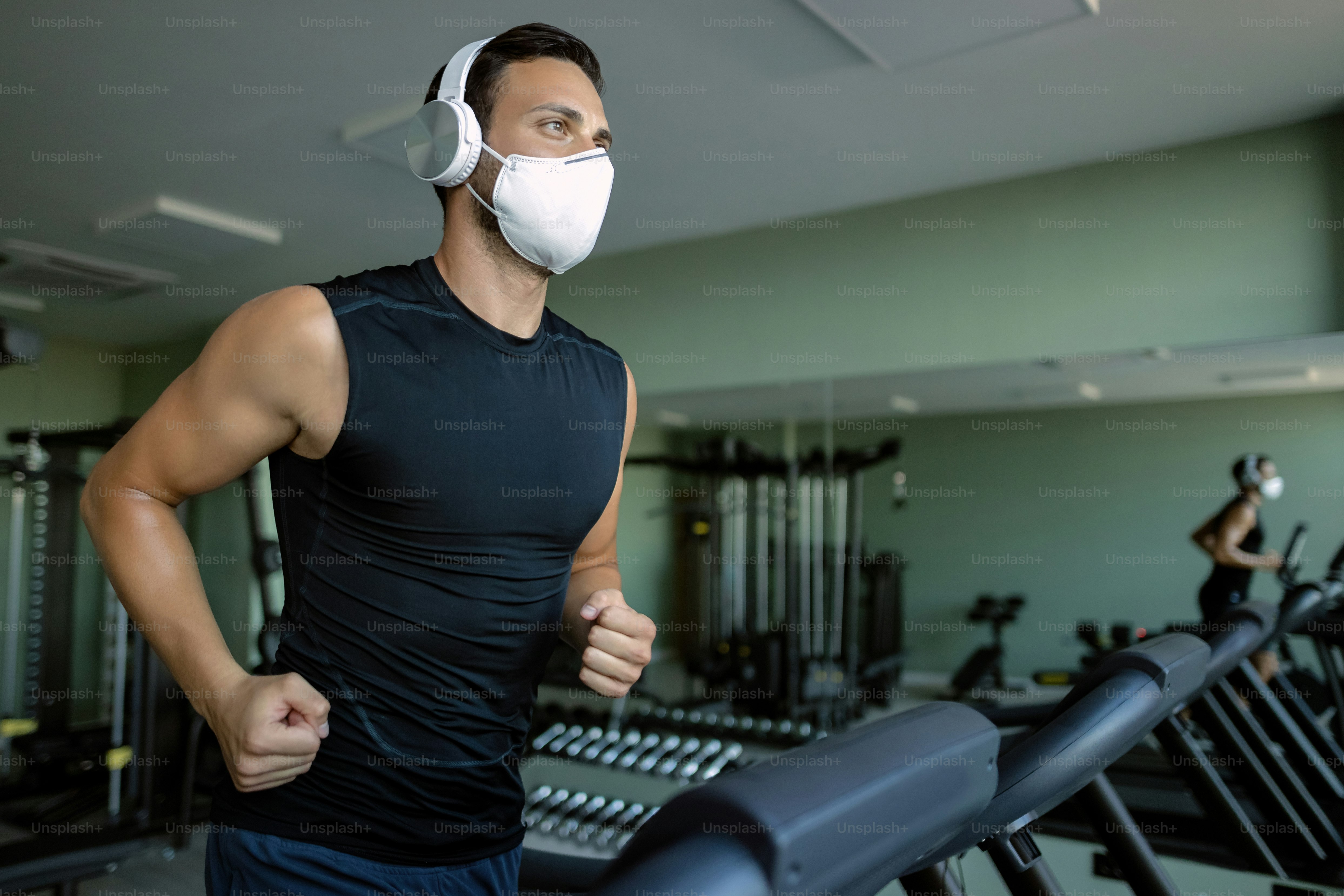 Young sportsman wearing a face mask while running on treadmill at ...