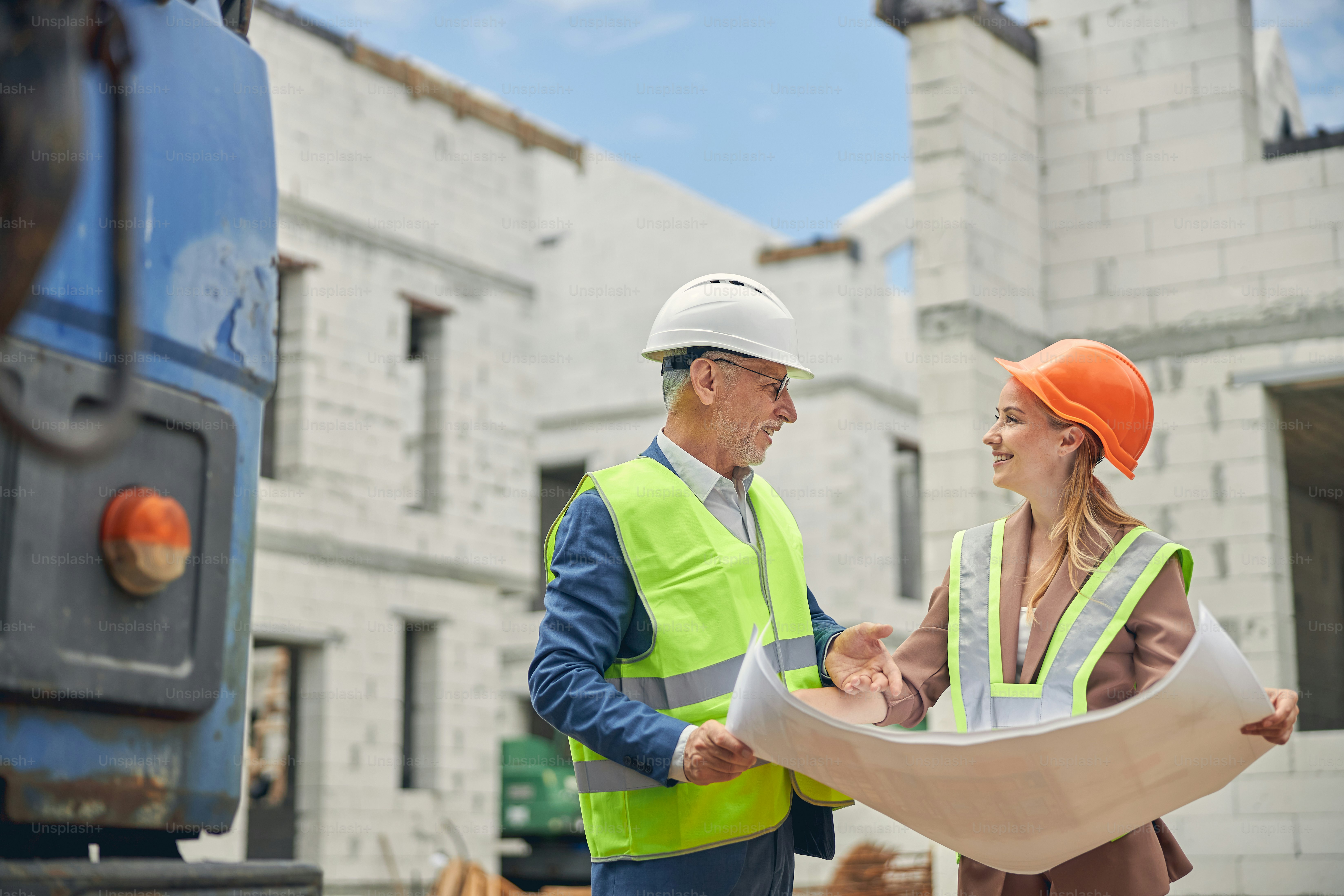 Joyful senior civil engineer and a smiling blonde female construction ...