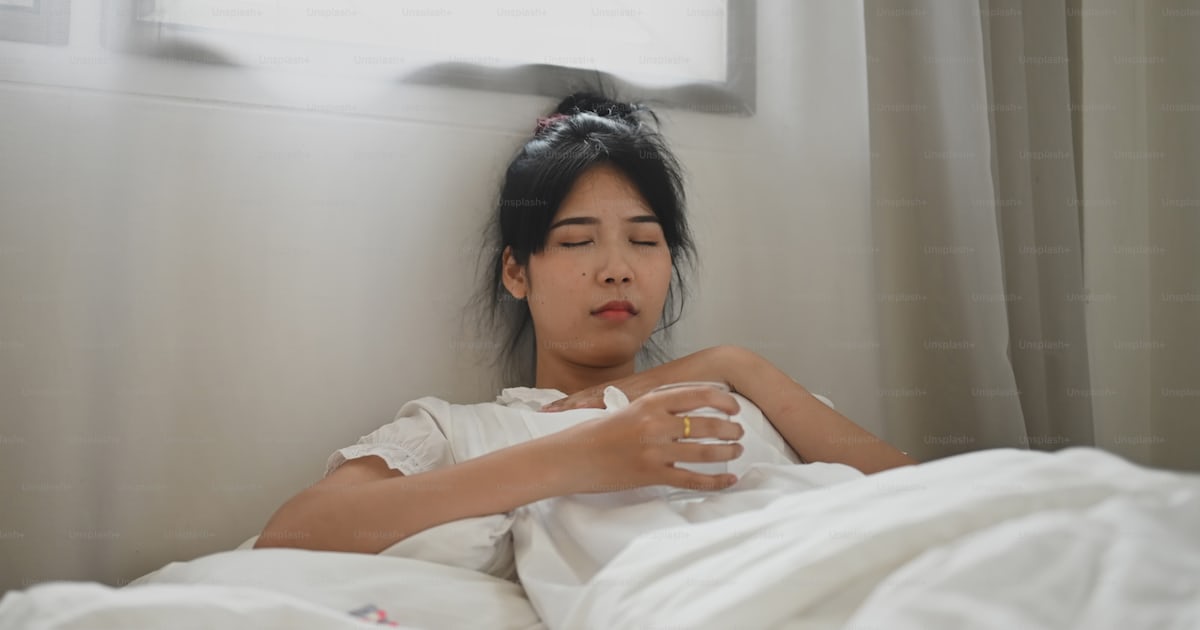 An Ill Woman Drinks Water And Consuming A Pill While Lying On The Bed