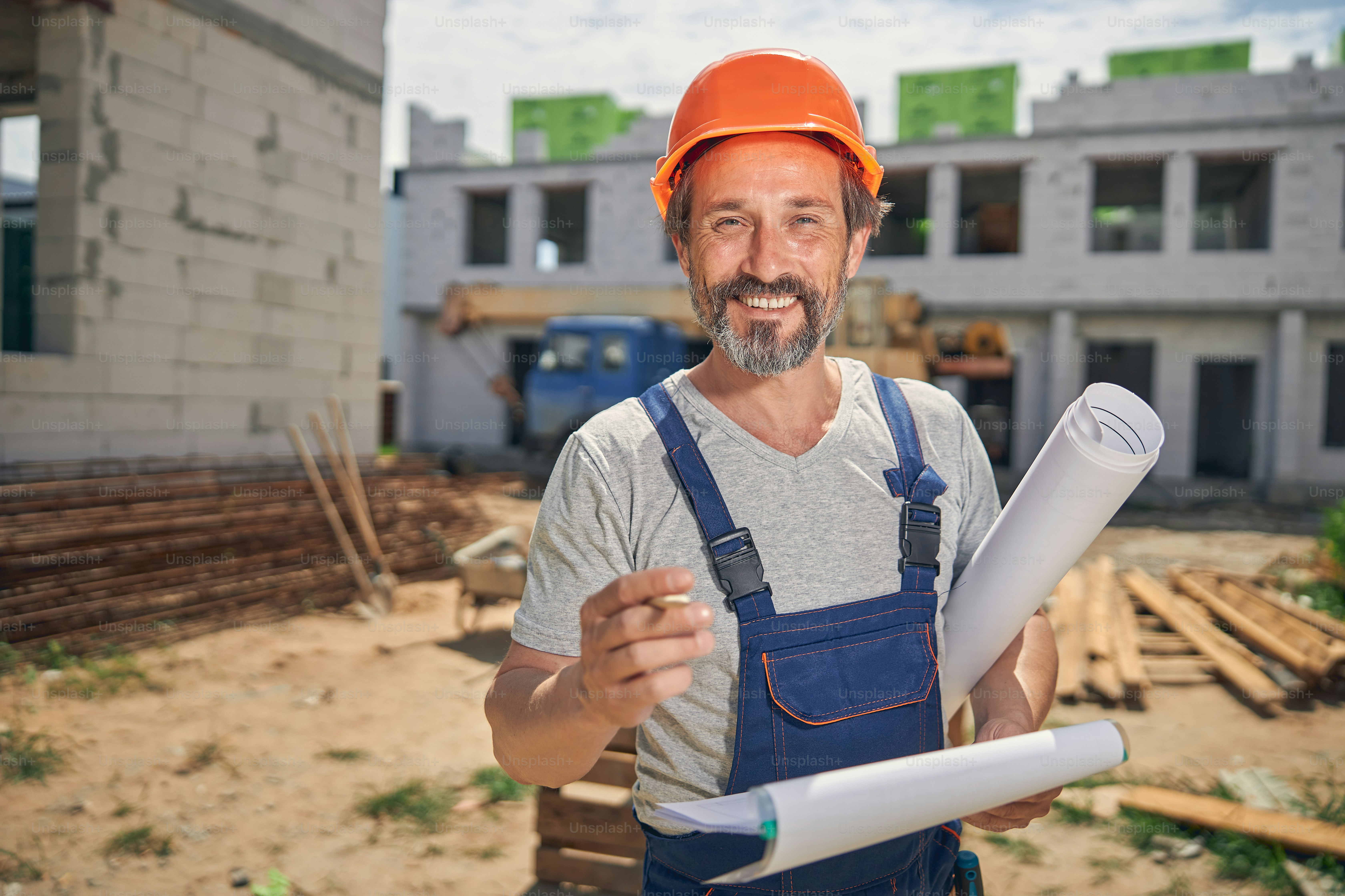 Vista frontal de un alegre ingeniero civil maduro con planos de casas ...