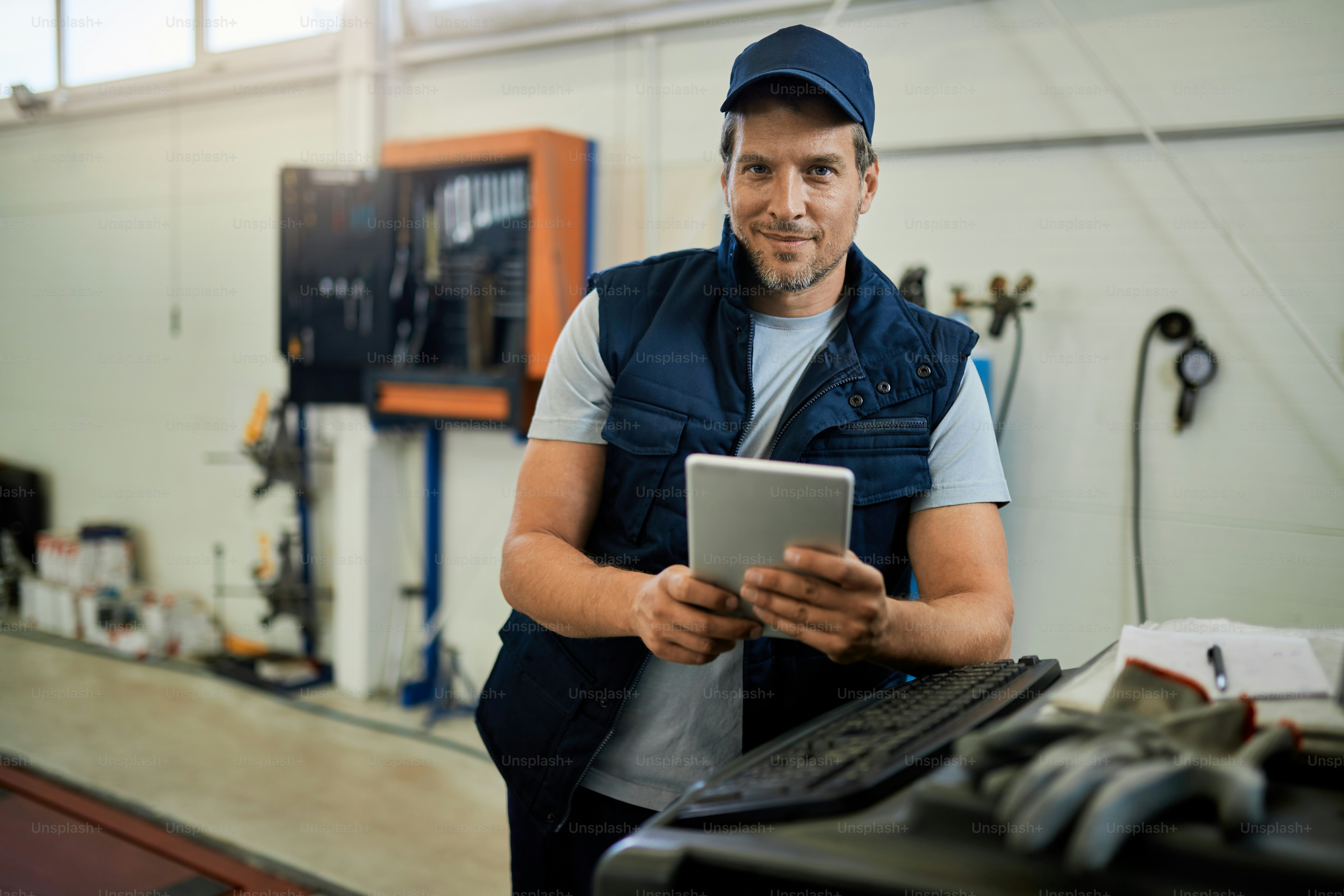 Happy auto repairman working on digital tablet in a workshop and ...
