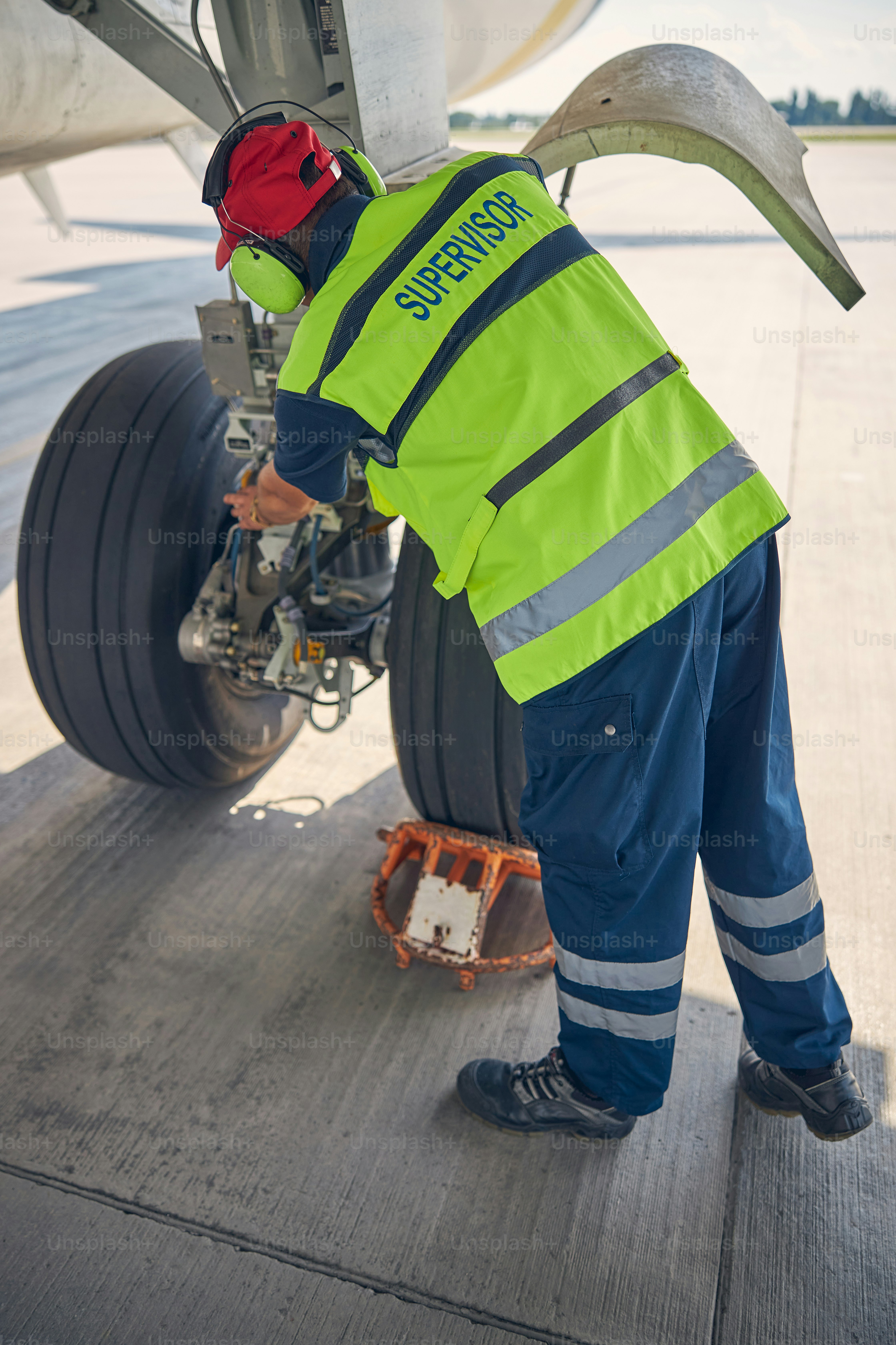 Back view of a qualified aircraft mechanic in a safety vest inspecting ...