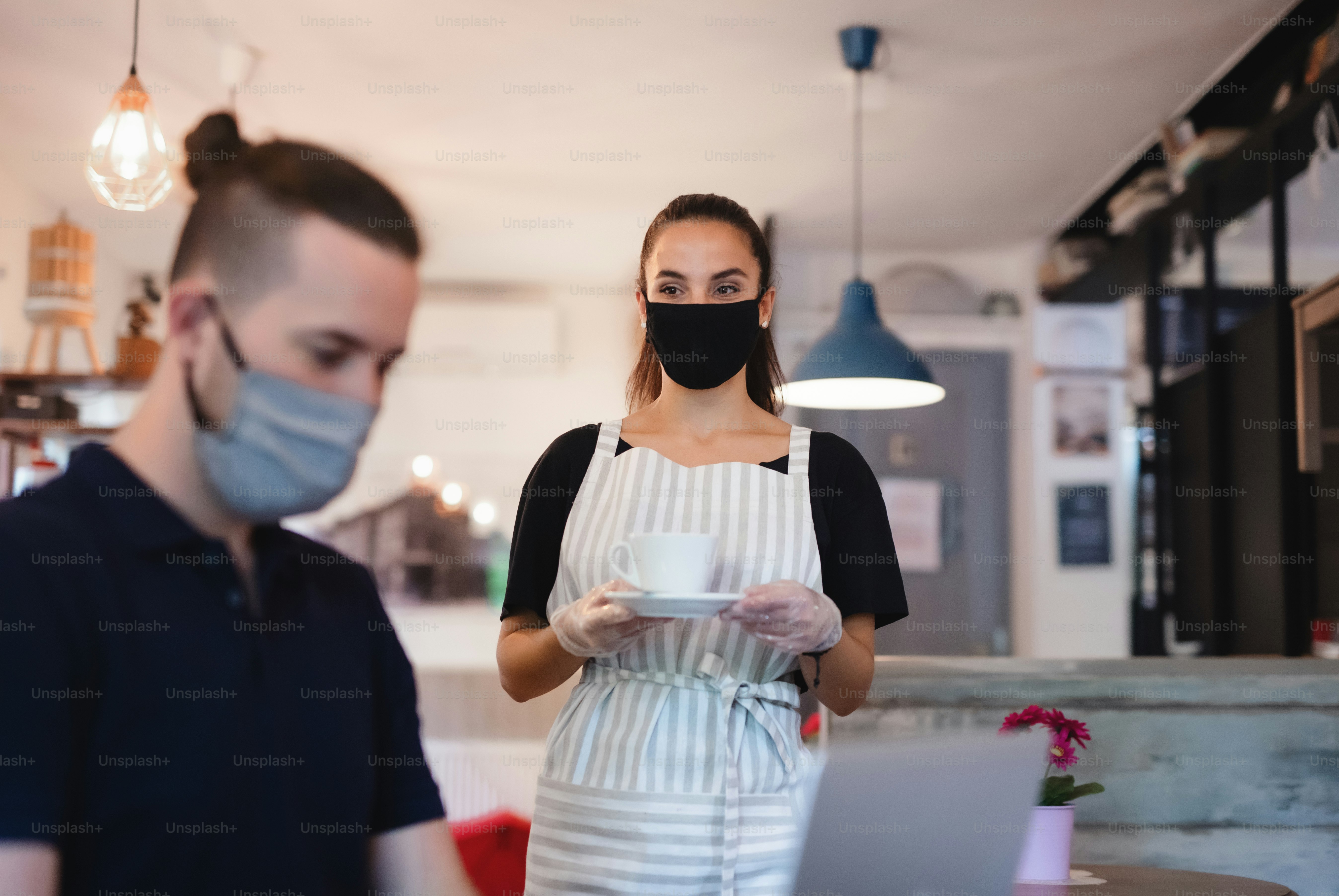 Young waitress with face mask working indoors in cafe, serving customer ...