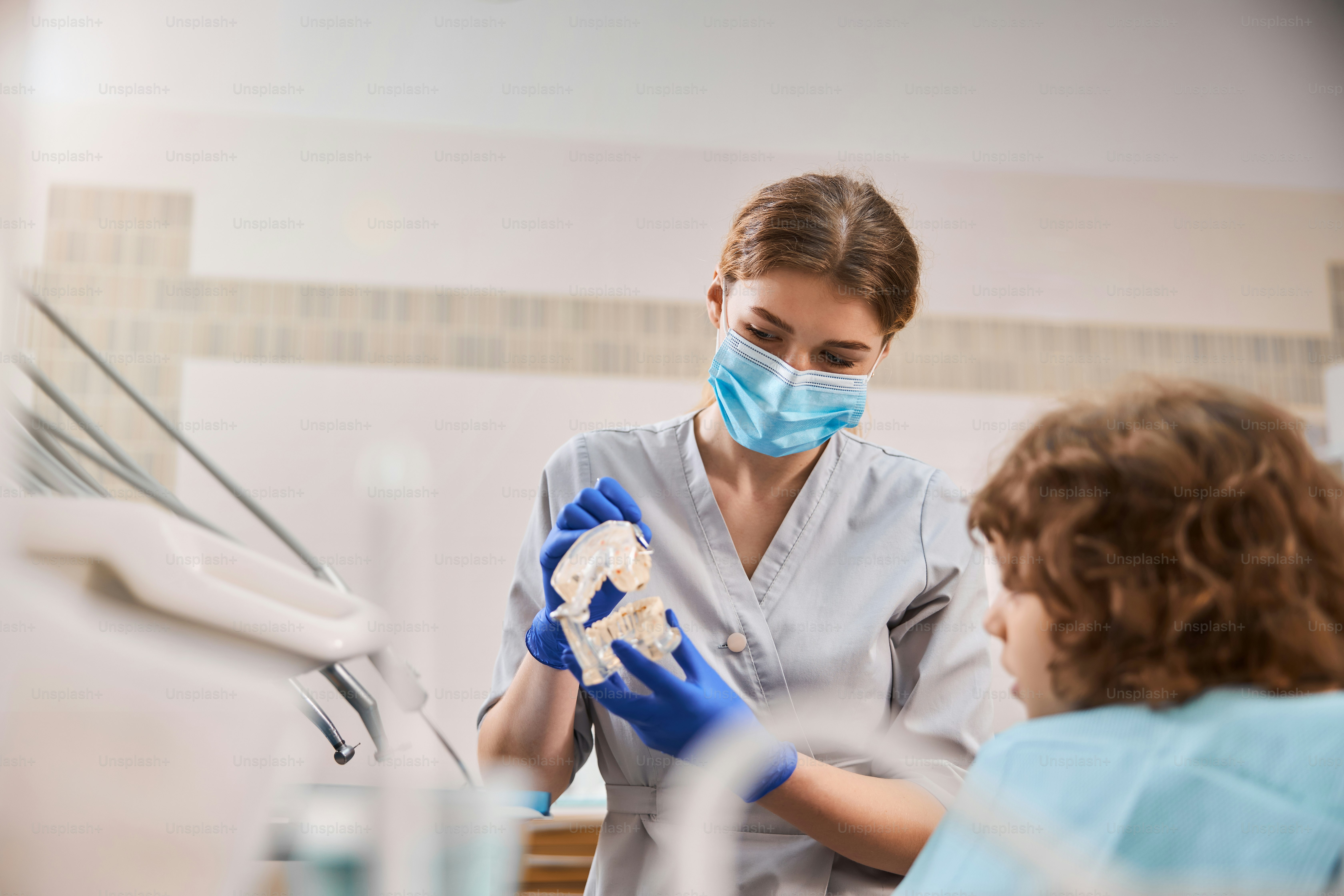 Curious kid looking attentively at teeth model while pediatric dentist ...