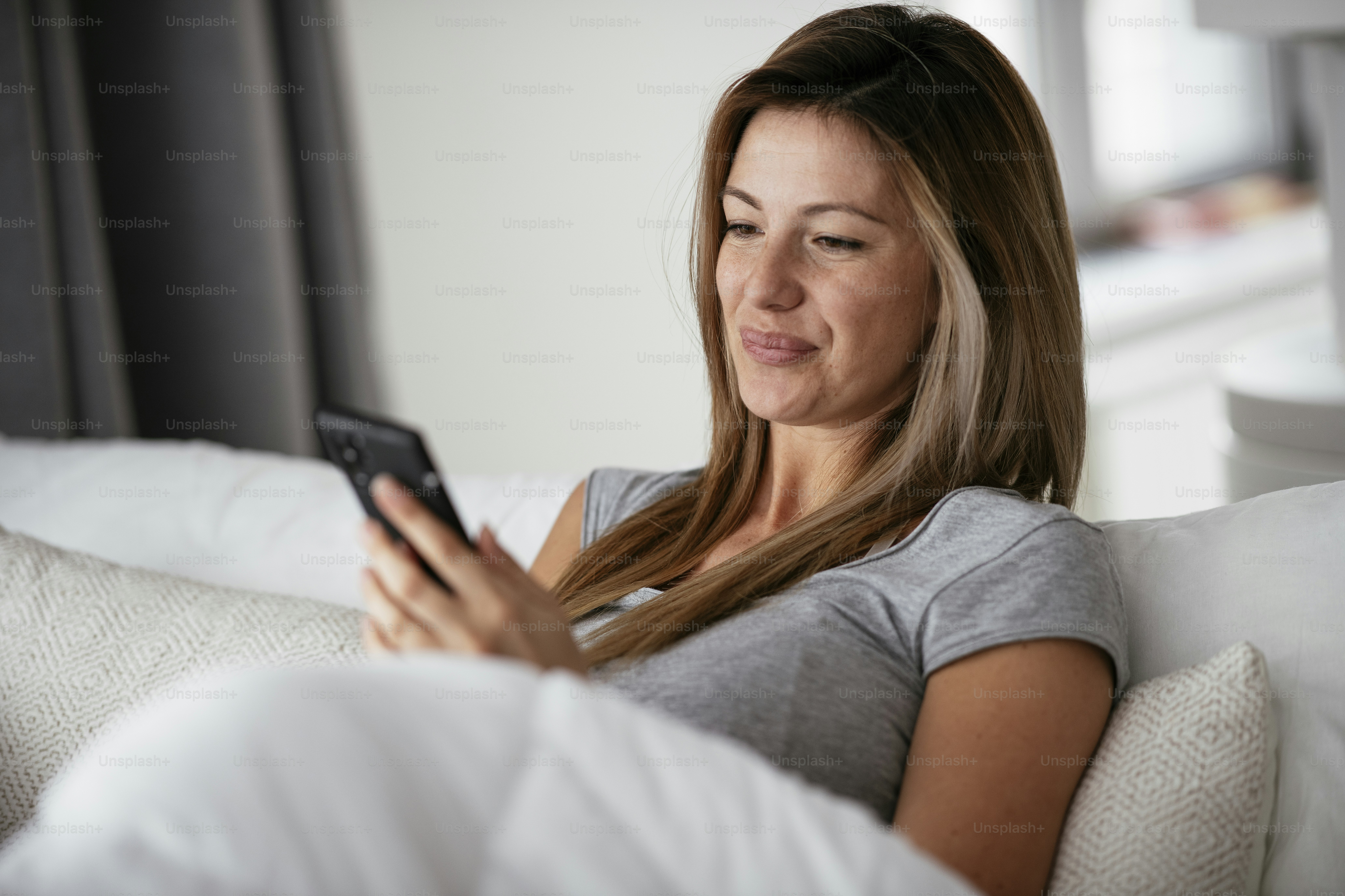Young beautiful woman using phone in bed. Girl lying on bed. photo ...