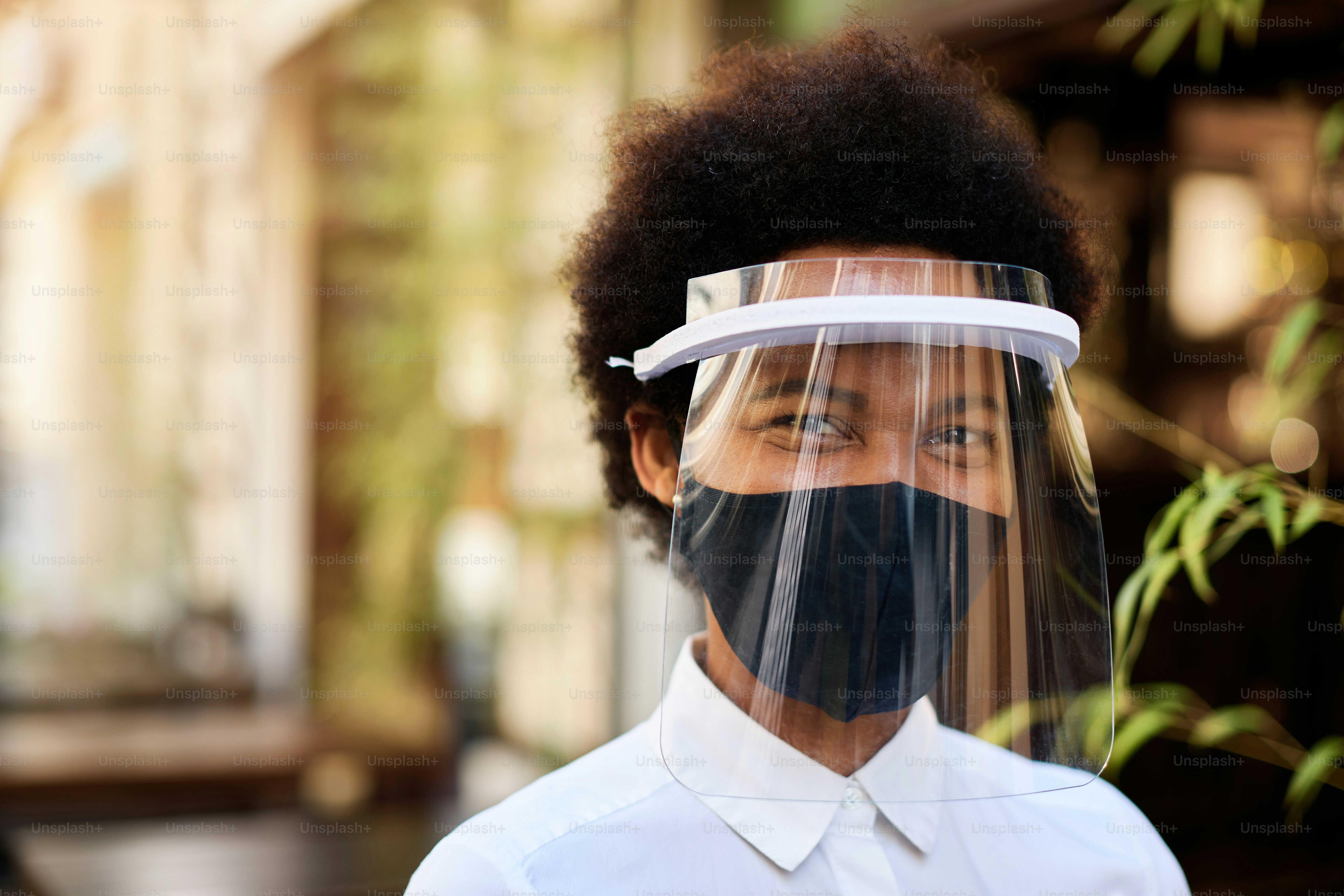 Happy African American waitress wearing protective face mask and visor ...