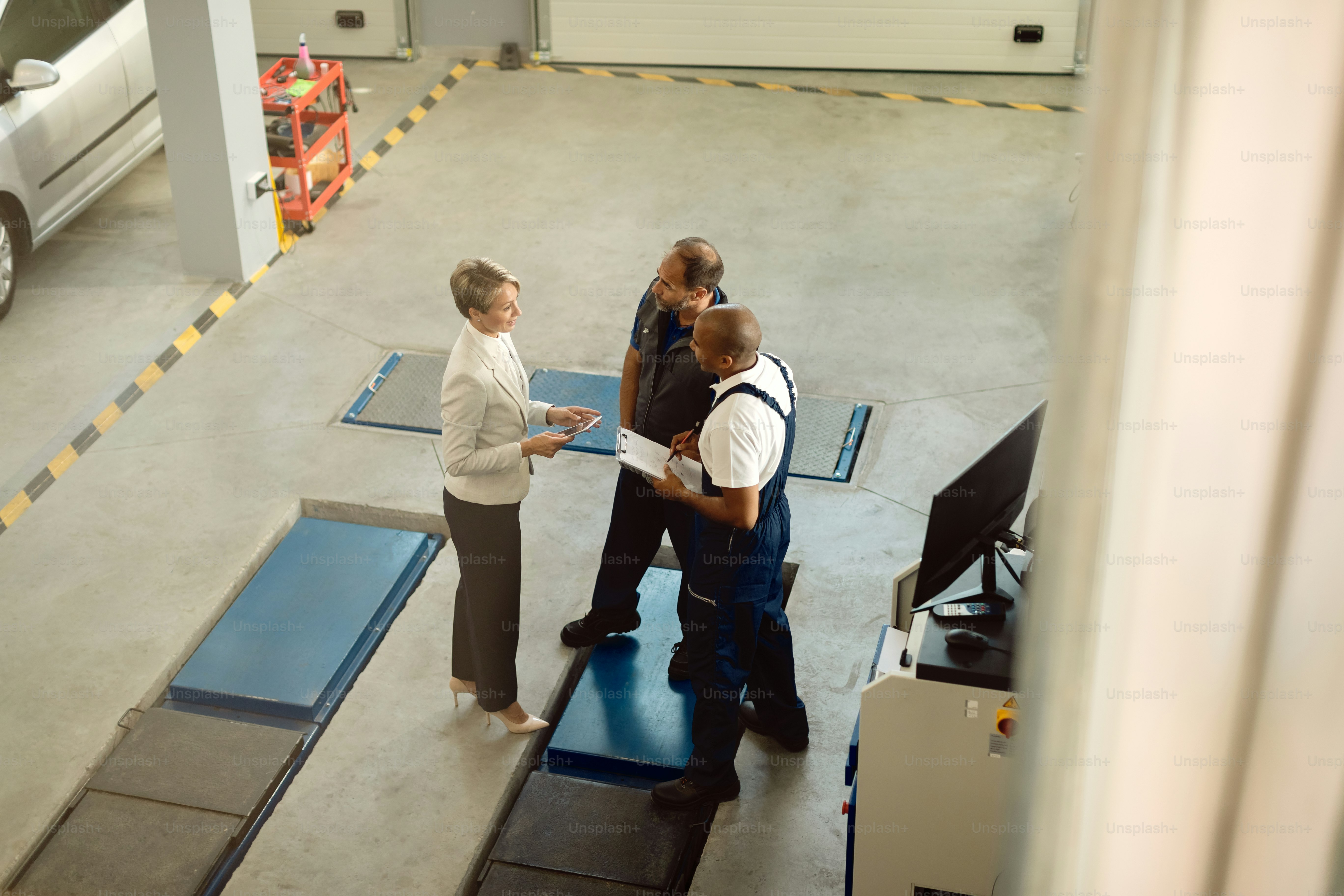 High angle view of auto mechanics communicating with a businesswoman in ...