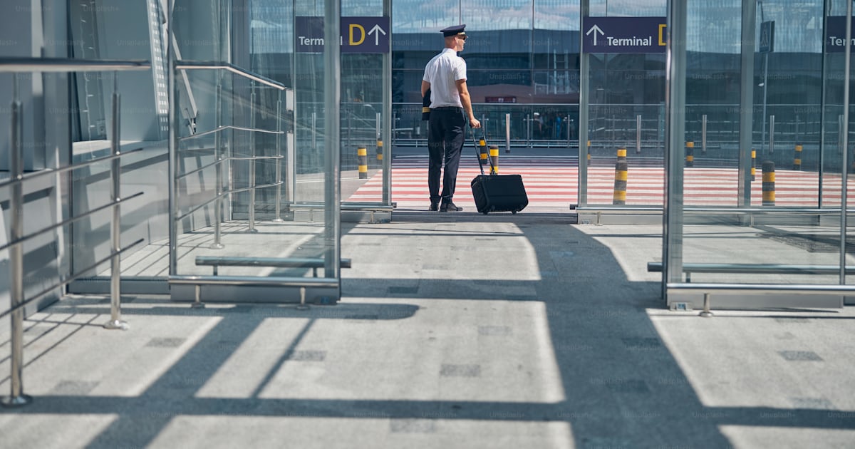 공항 터미널 출구 문에 서 있는 트롤리 수하물 가방을 든 항공사 직원 사진 Unsplash의 공항 이미지