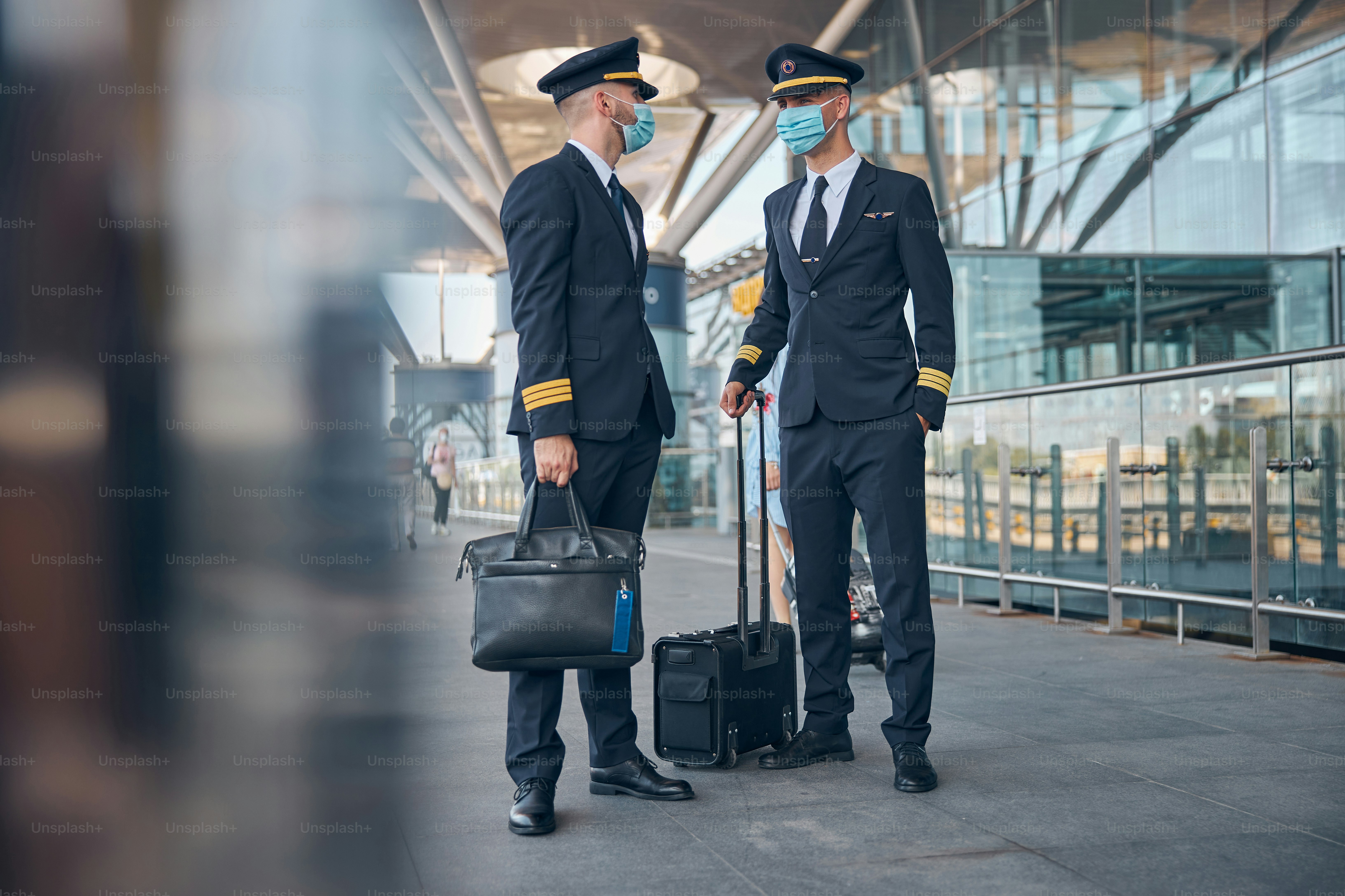Two handsome young men airline workers in protective face masks waiting ...