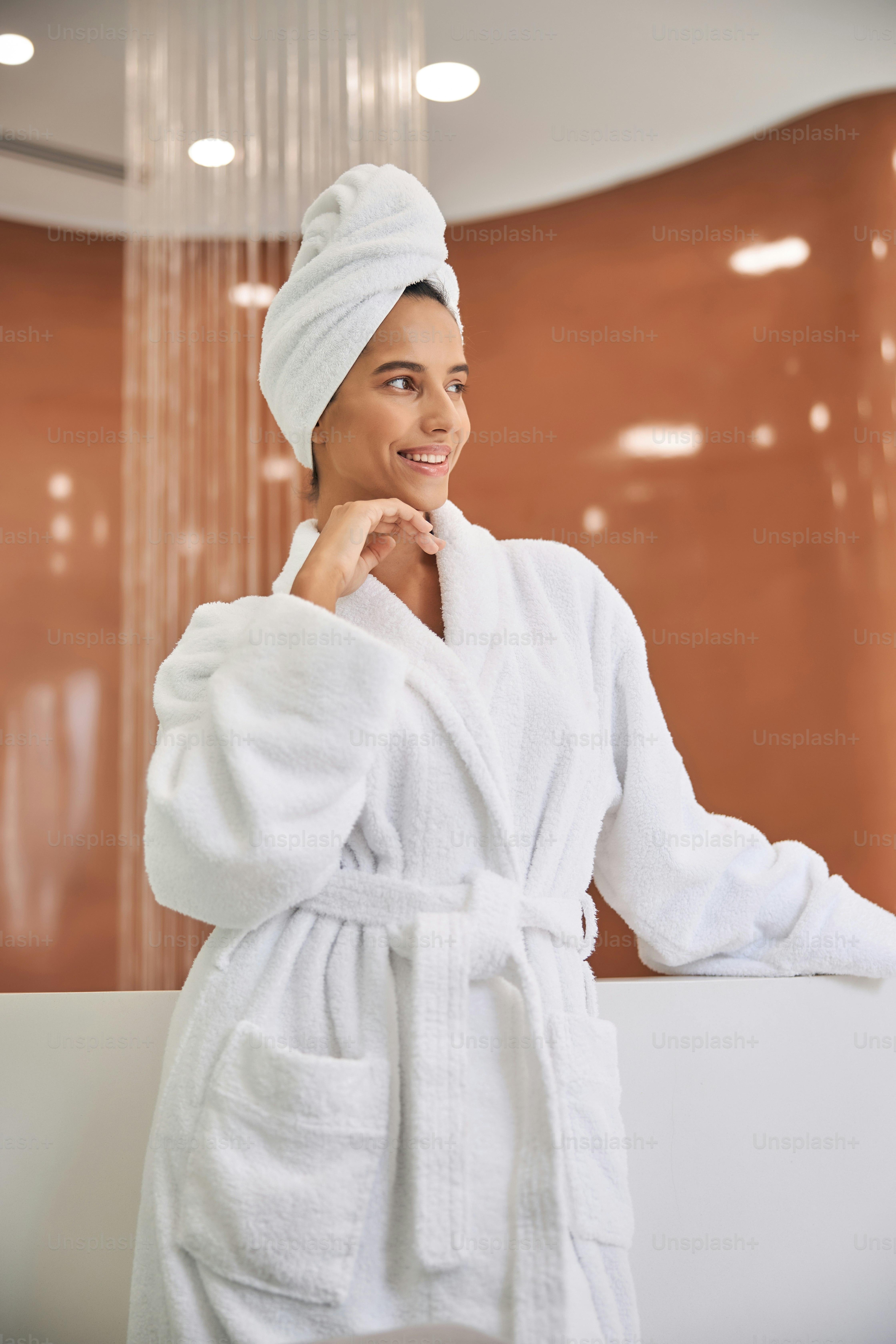 Pretty lady with towel on her head wearing white soft bathrobe while ...
