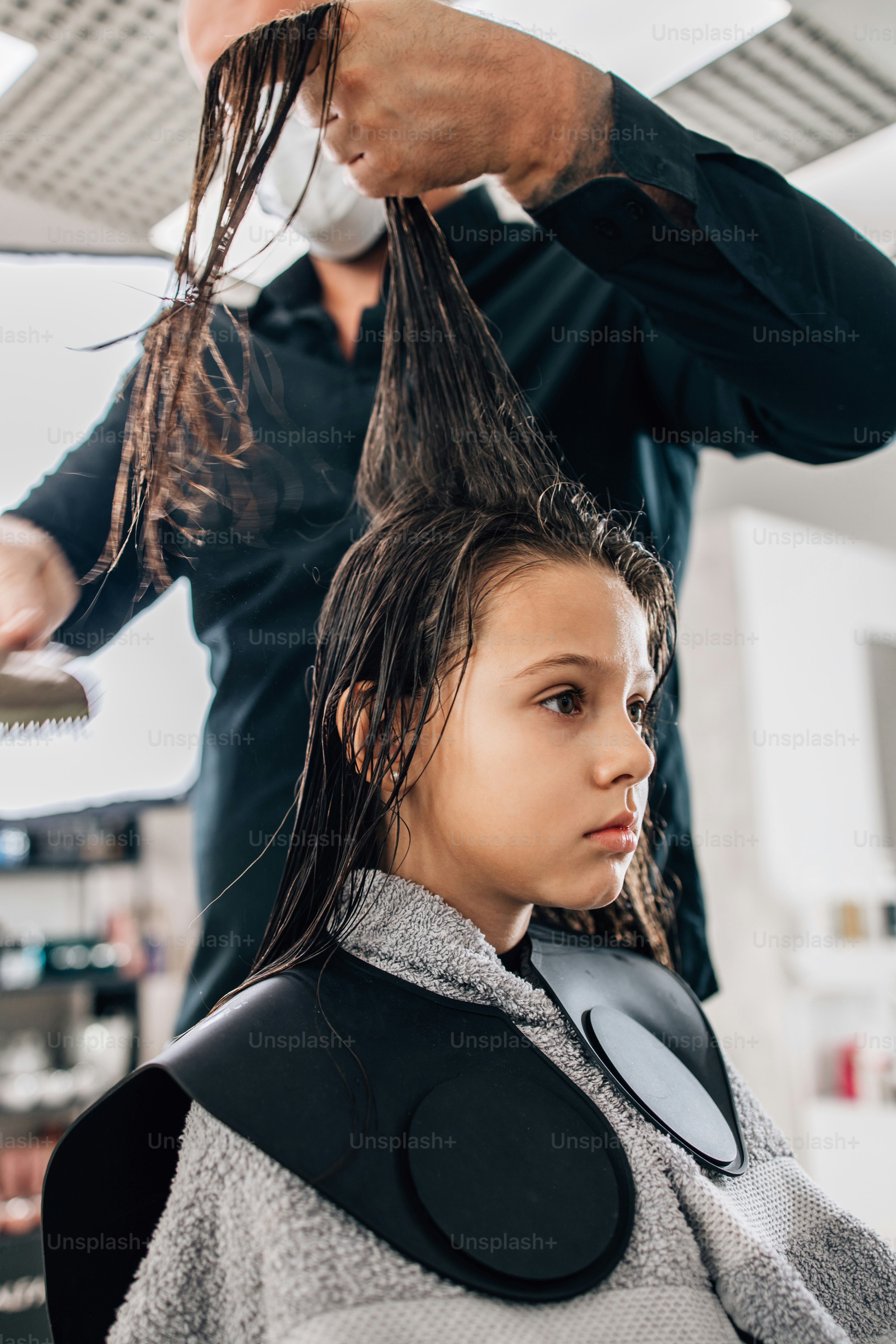 Young girl at hairstyle treatment while professional hairdresser gently ...