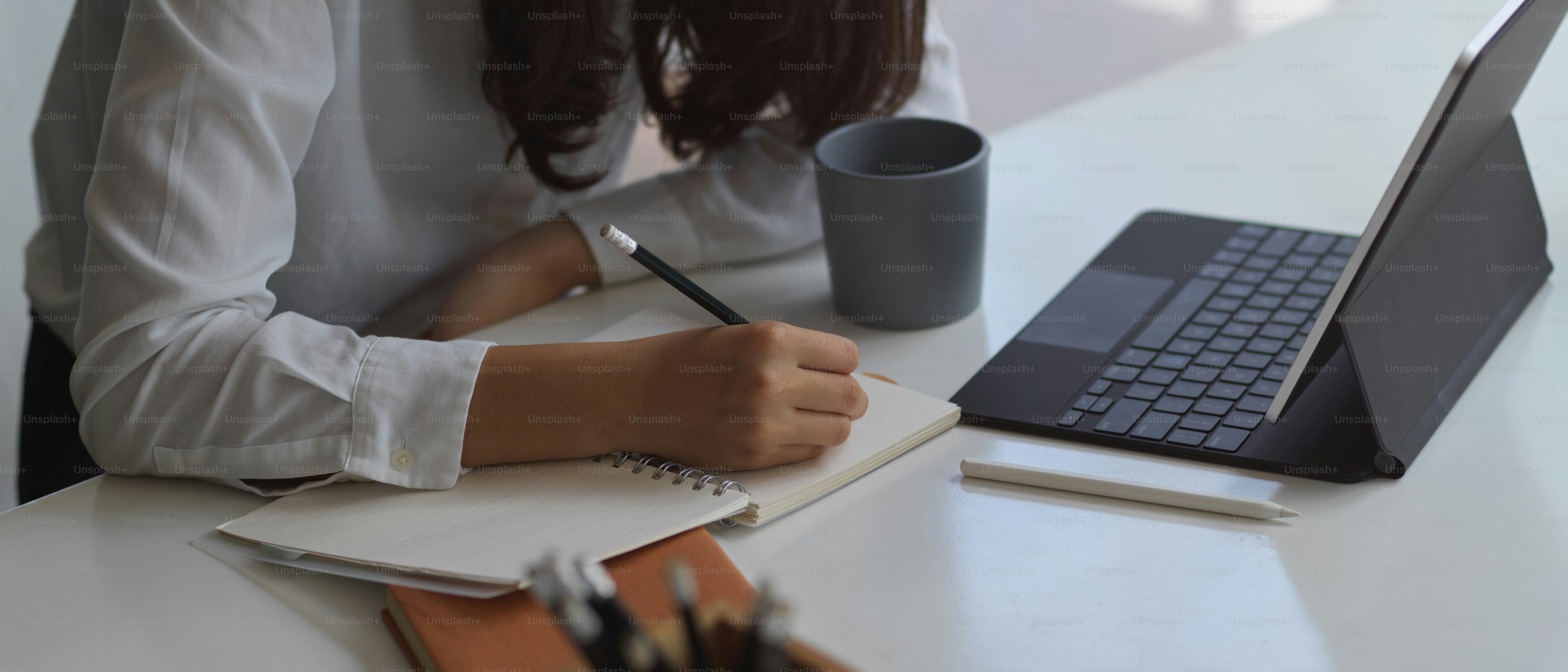 Cropped shot of female writing on blank notebook with pencil while ...
