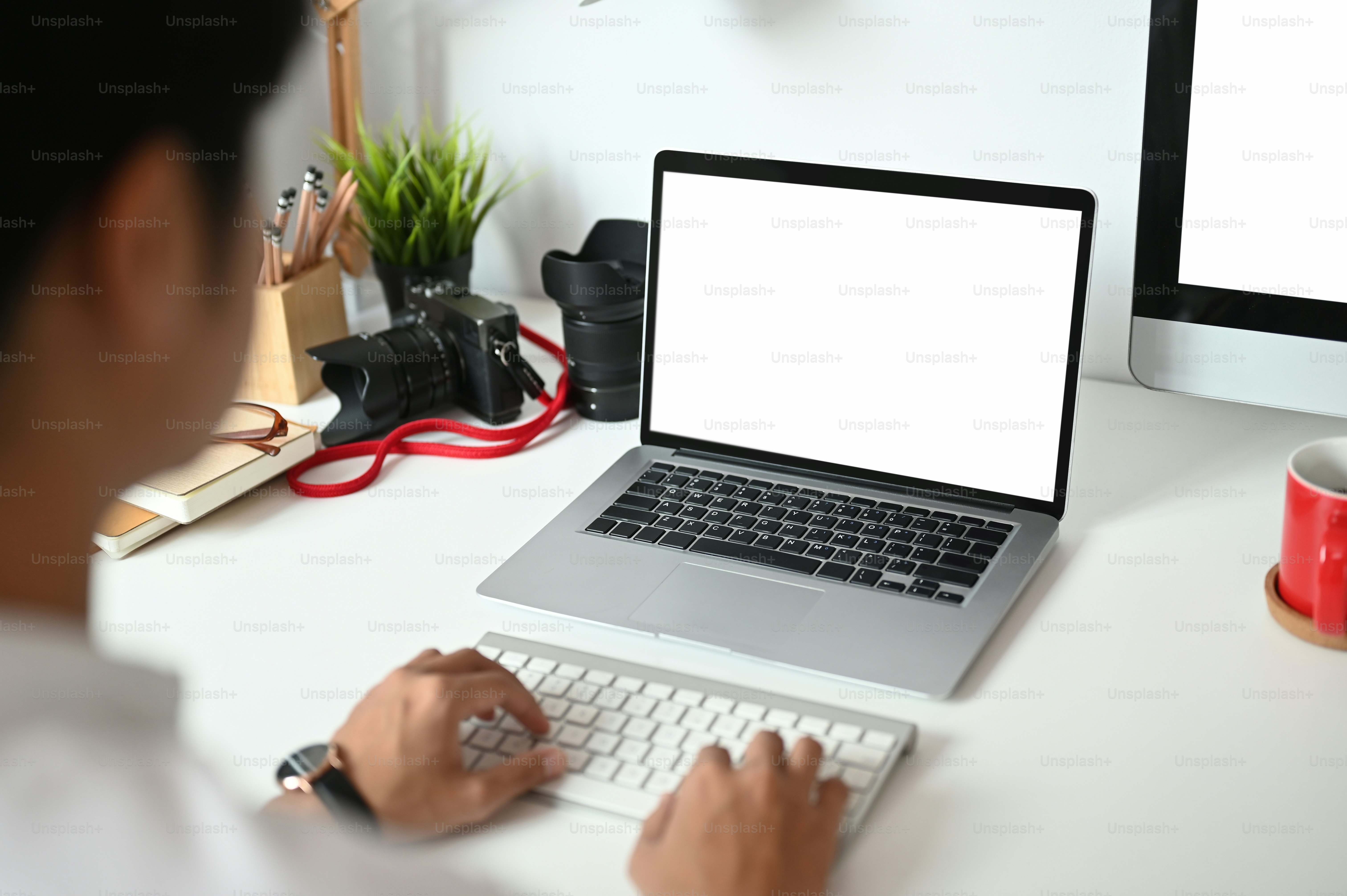 A young photographer using laptop with white screen on his work space ...