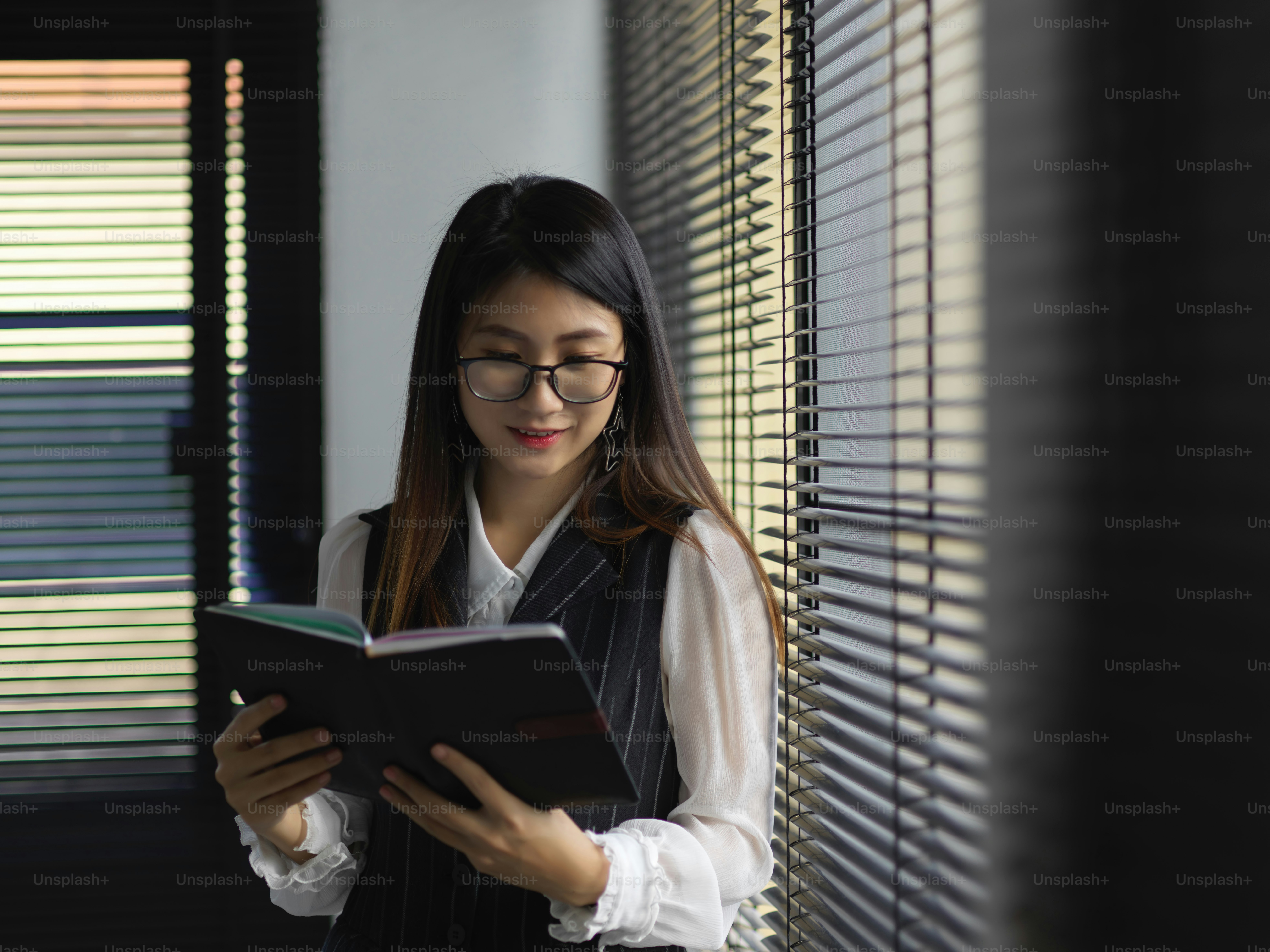 Portrait of female office worker reading schedule book while standing ...