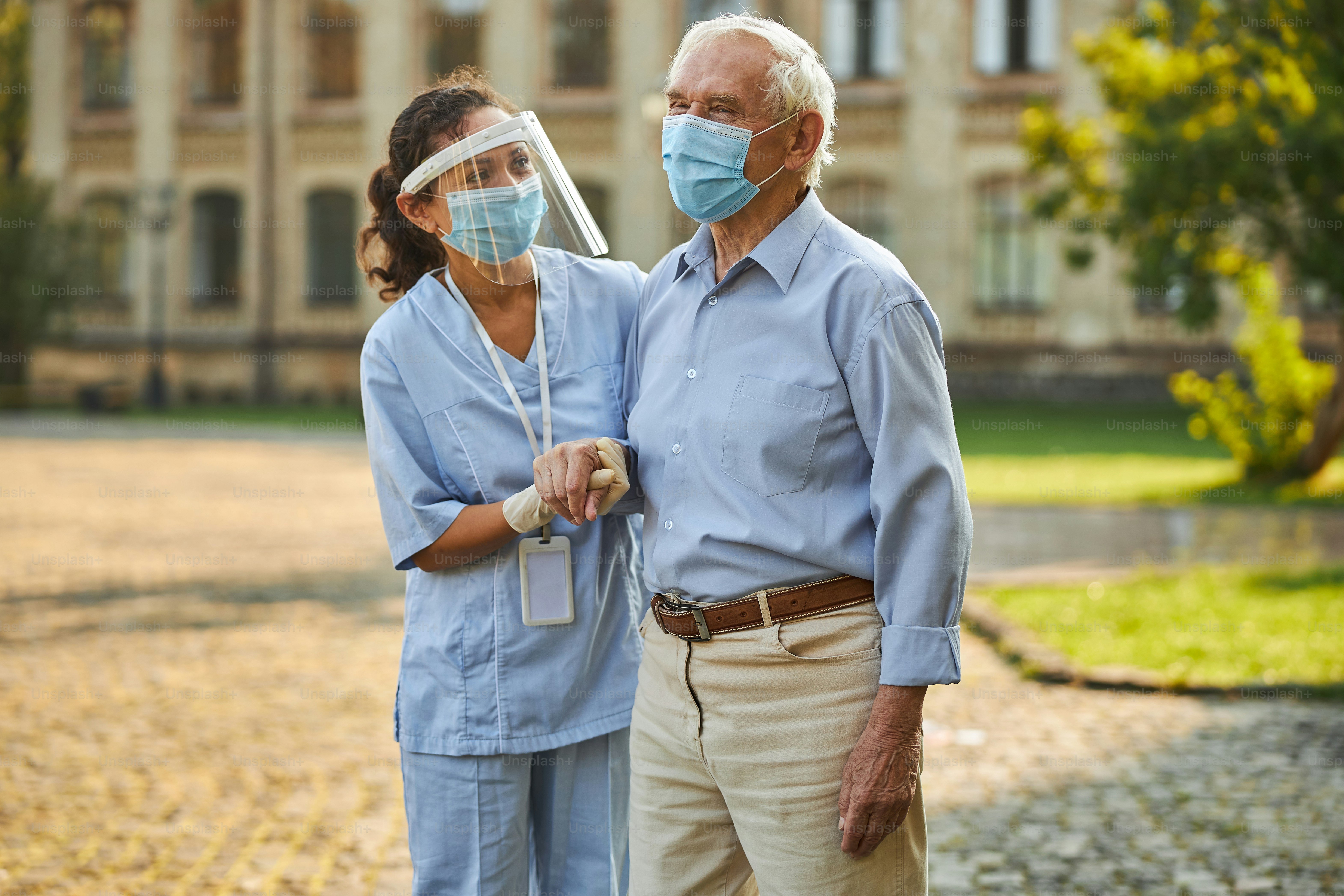 Doctor and old patient wearing masks and standing outdoors while ...