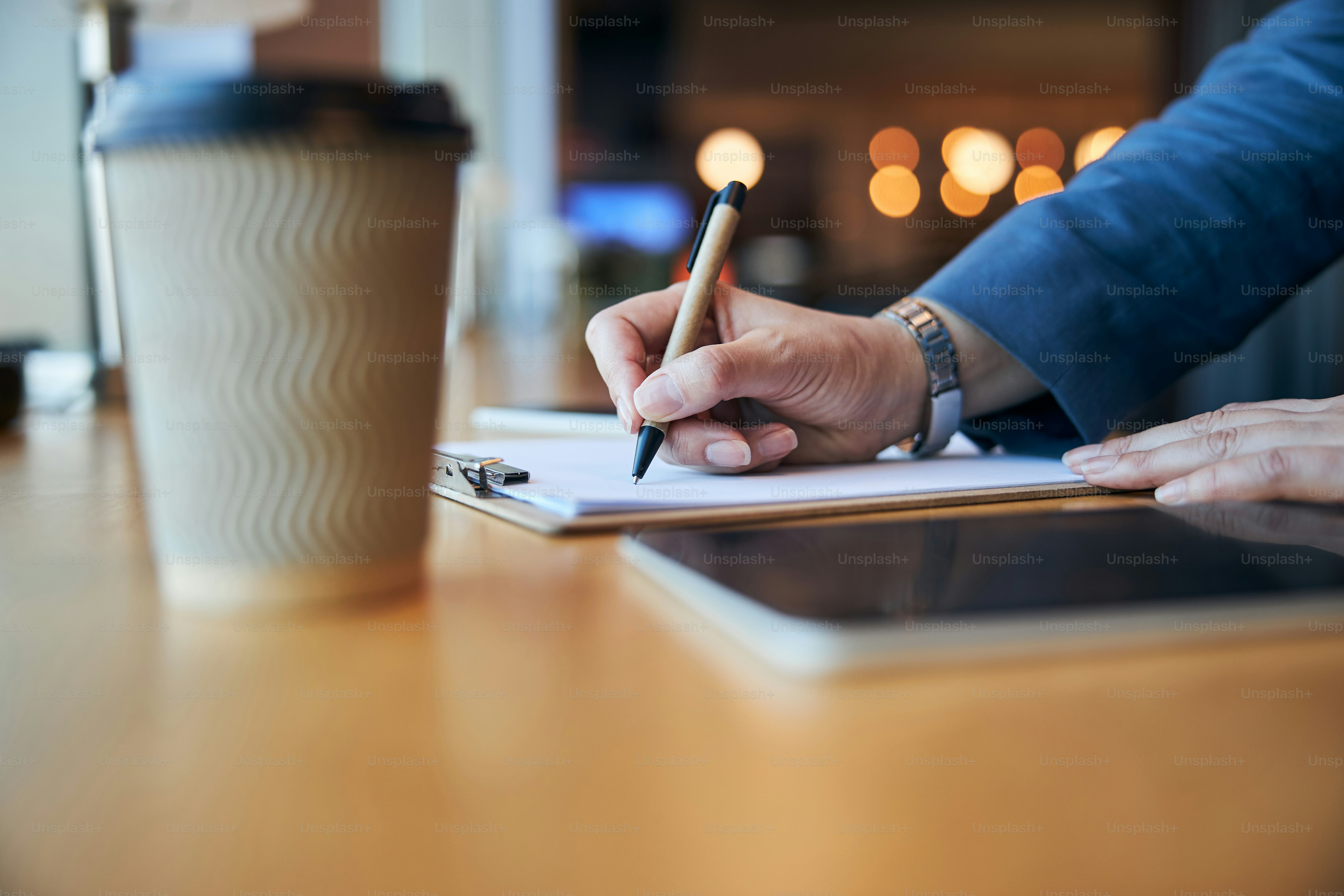Close up of female hand taking notes while lady sitting at wooden desk ...