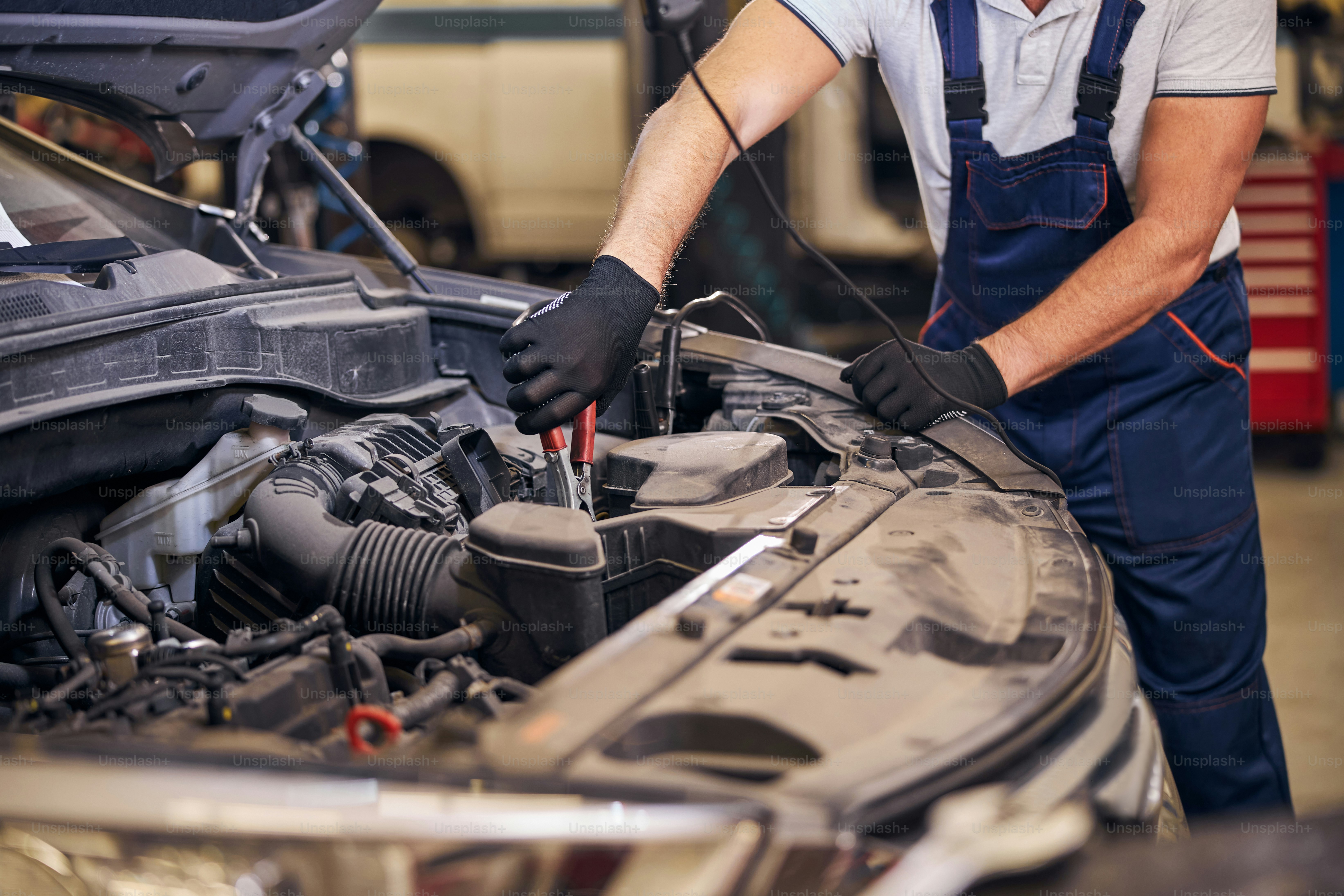 Auto mechanic in black gloves using pliers while fixing car engine in ...