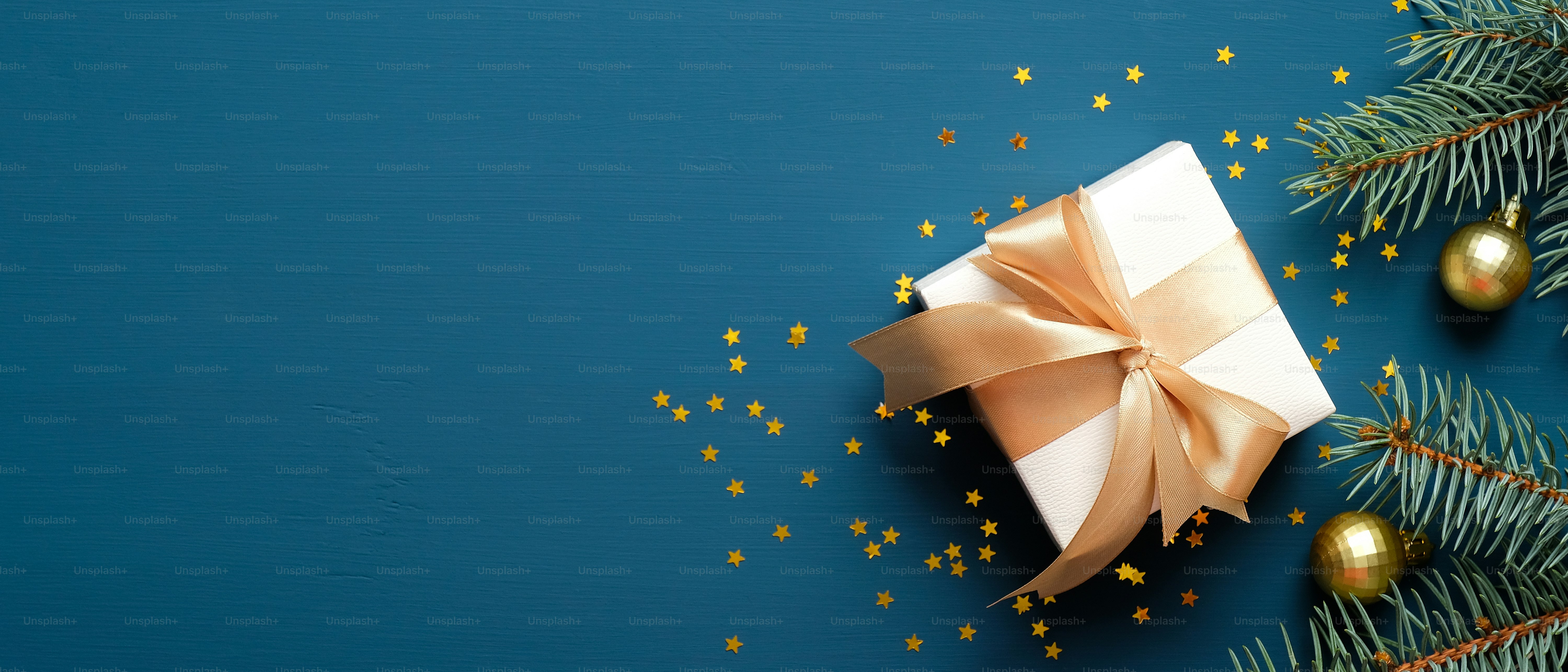 White gift box with golden ribbon bow, fir branches decorated balls and ...