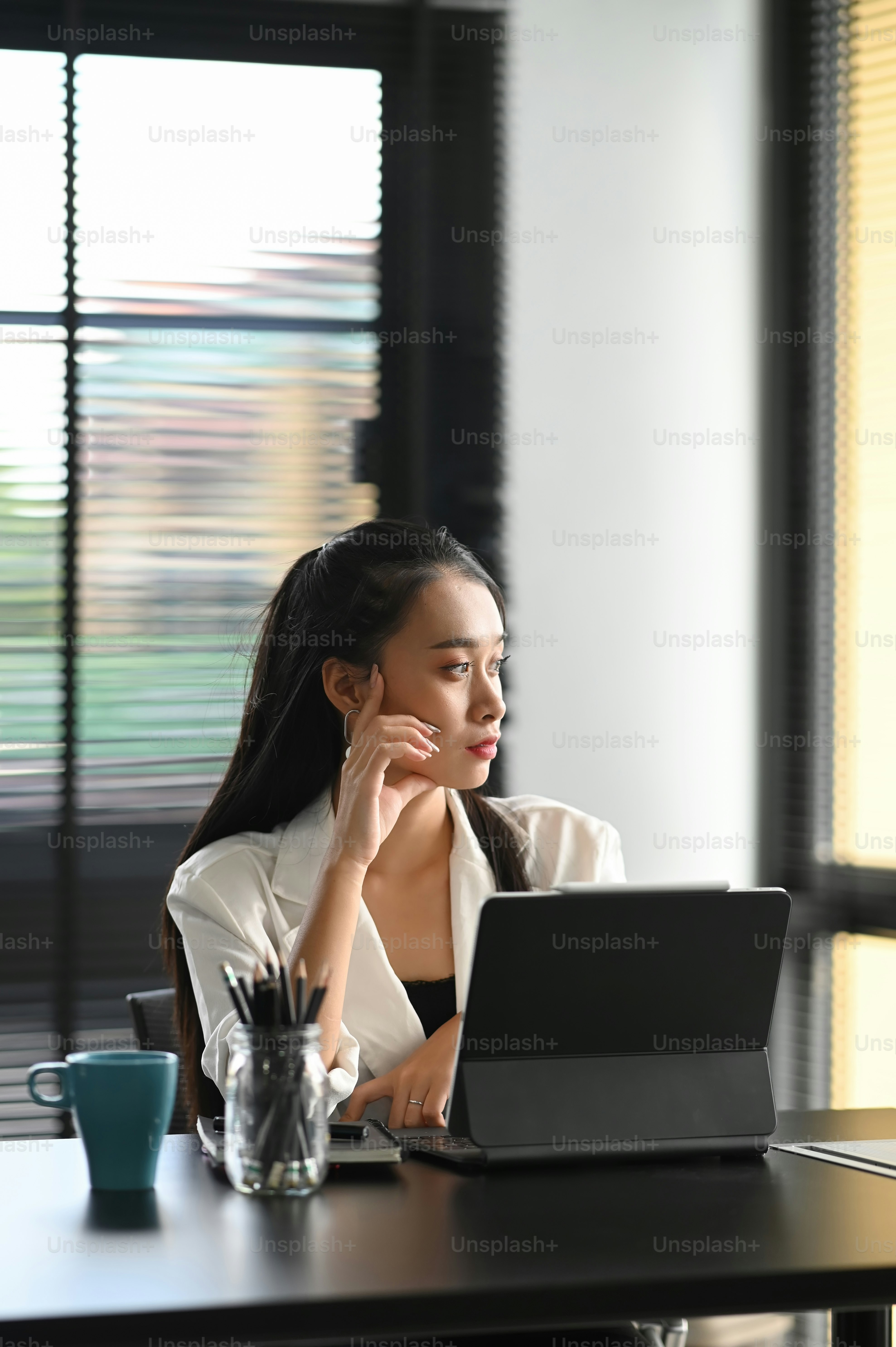 Portrait of thoughtful businesswoman sitting in office while looking ...