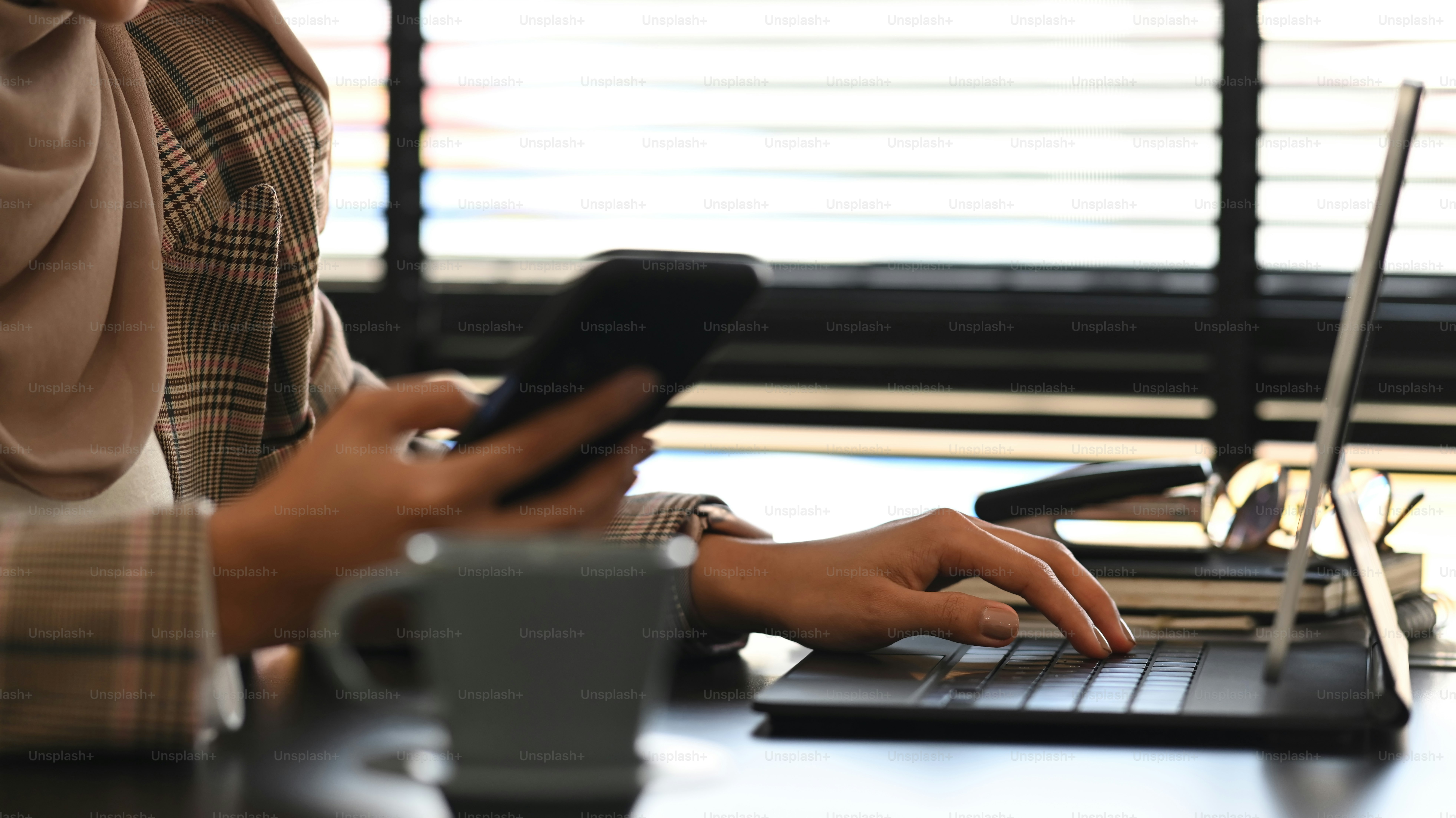 Cropped shot of woman hands using smart phone while working on computer ...