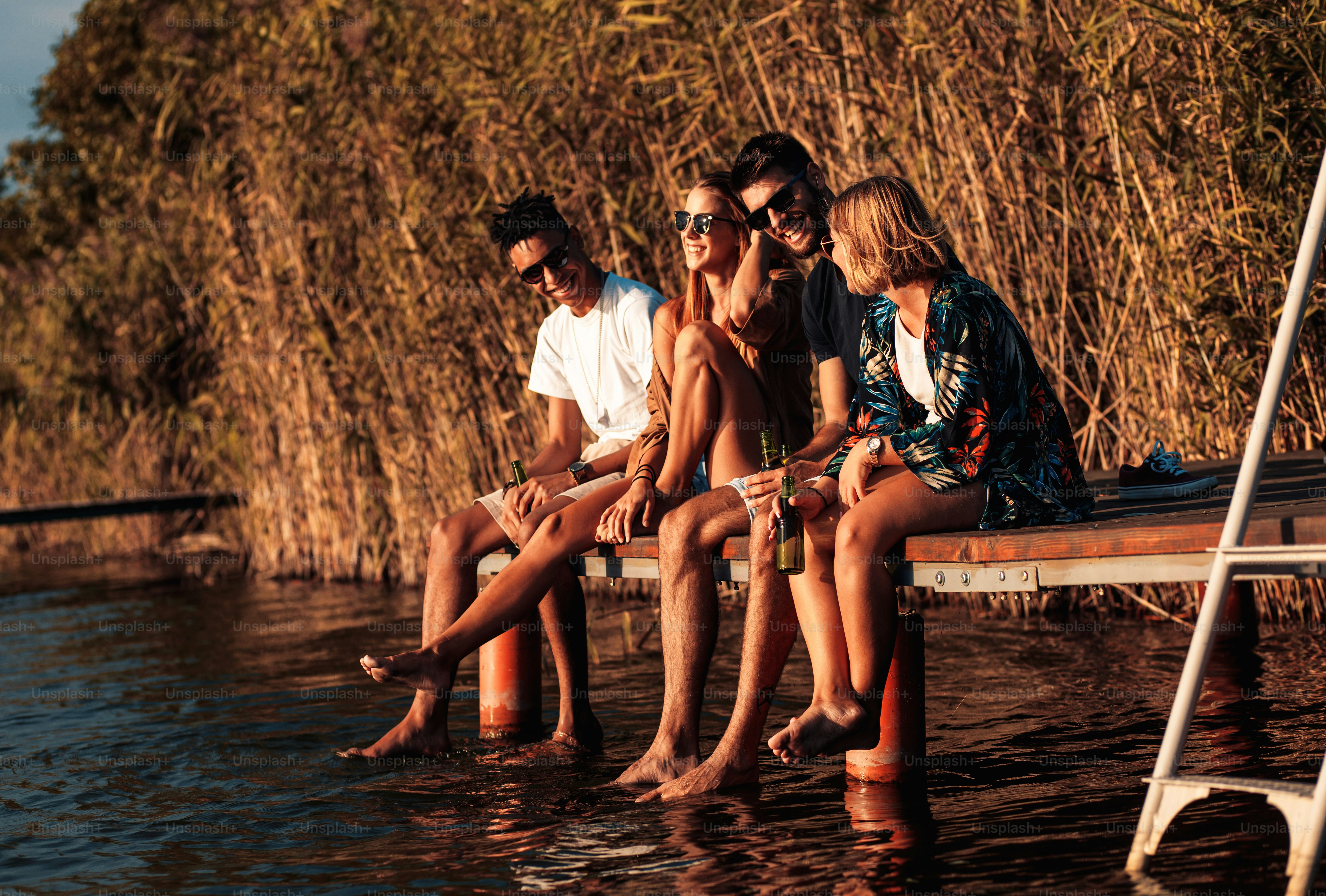 Group of friends enjoying a day at the lake. They sitting on pier ...