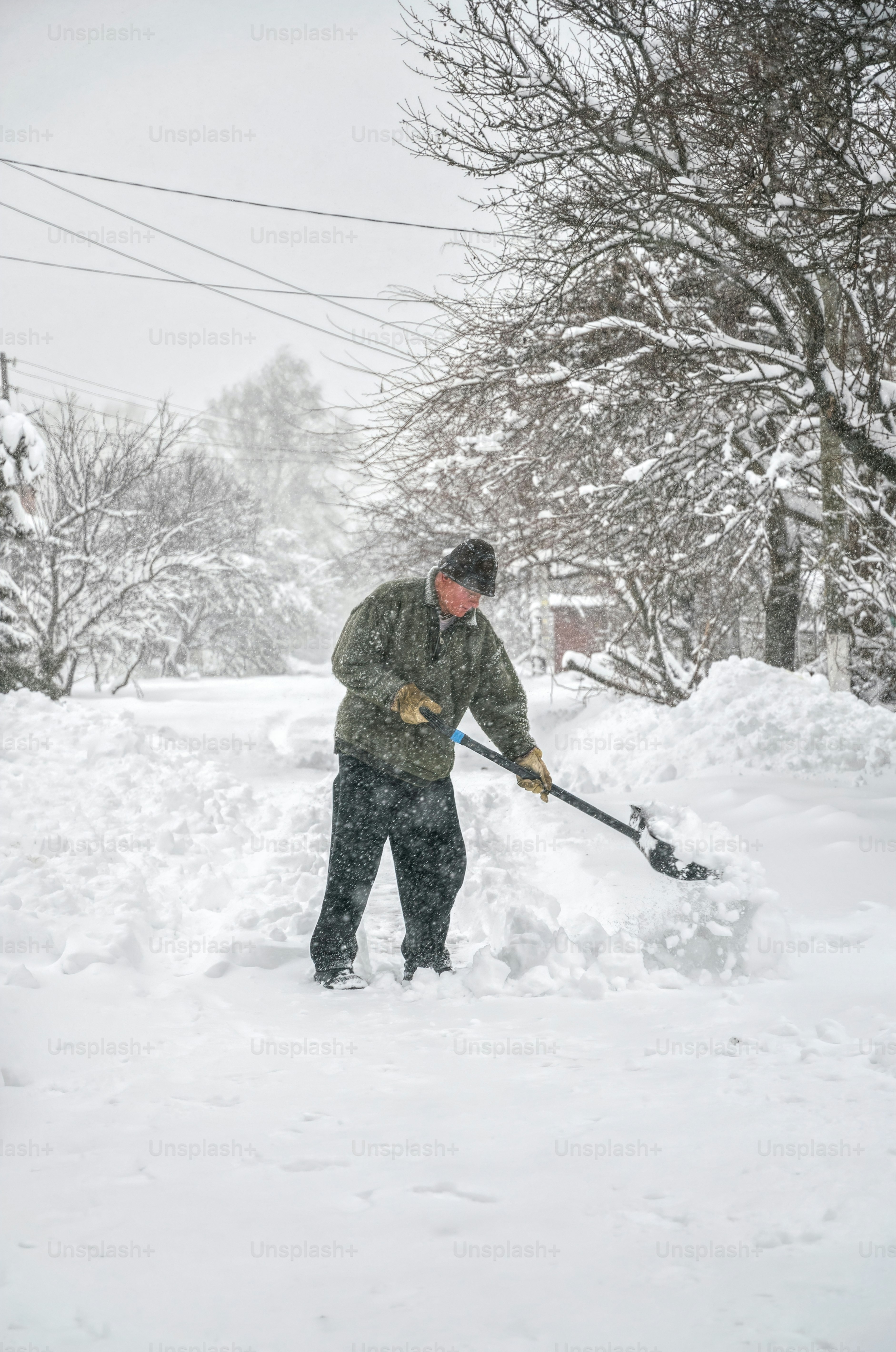 Elderly man with a shovel in his hands clears the street after a heavy ...