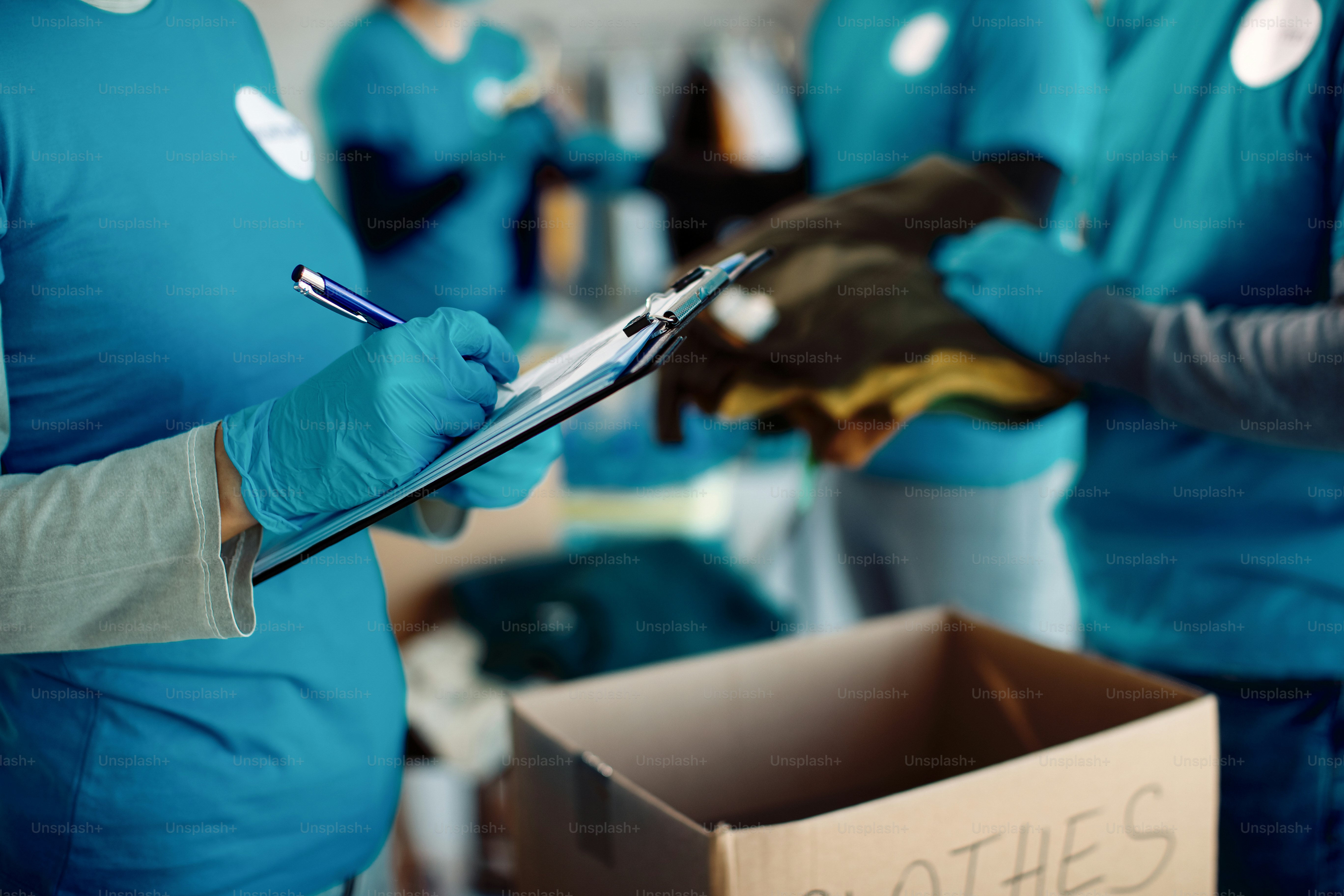 Close-up of woman taking notes while volunteers are packing donation ...